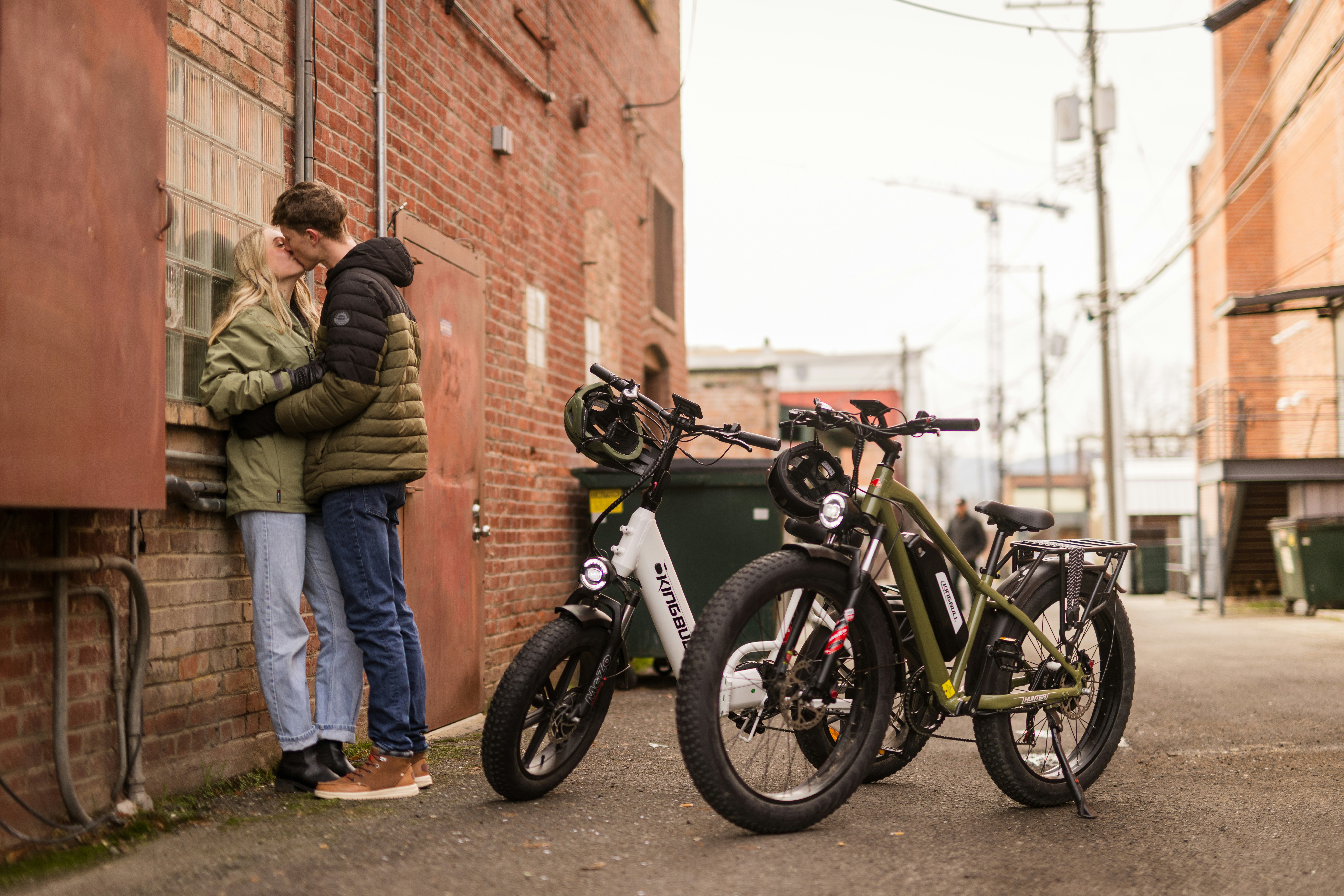 Couple kissing by brick wall with electric bikes
