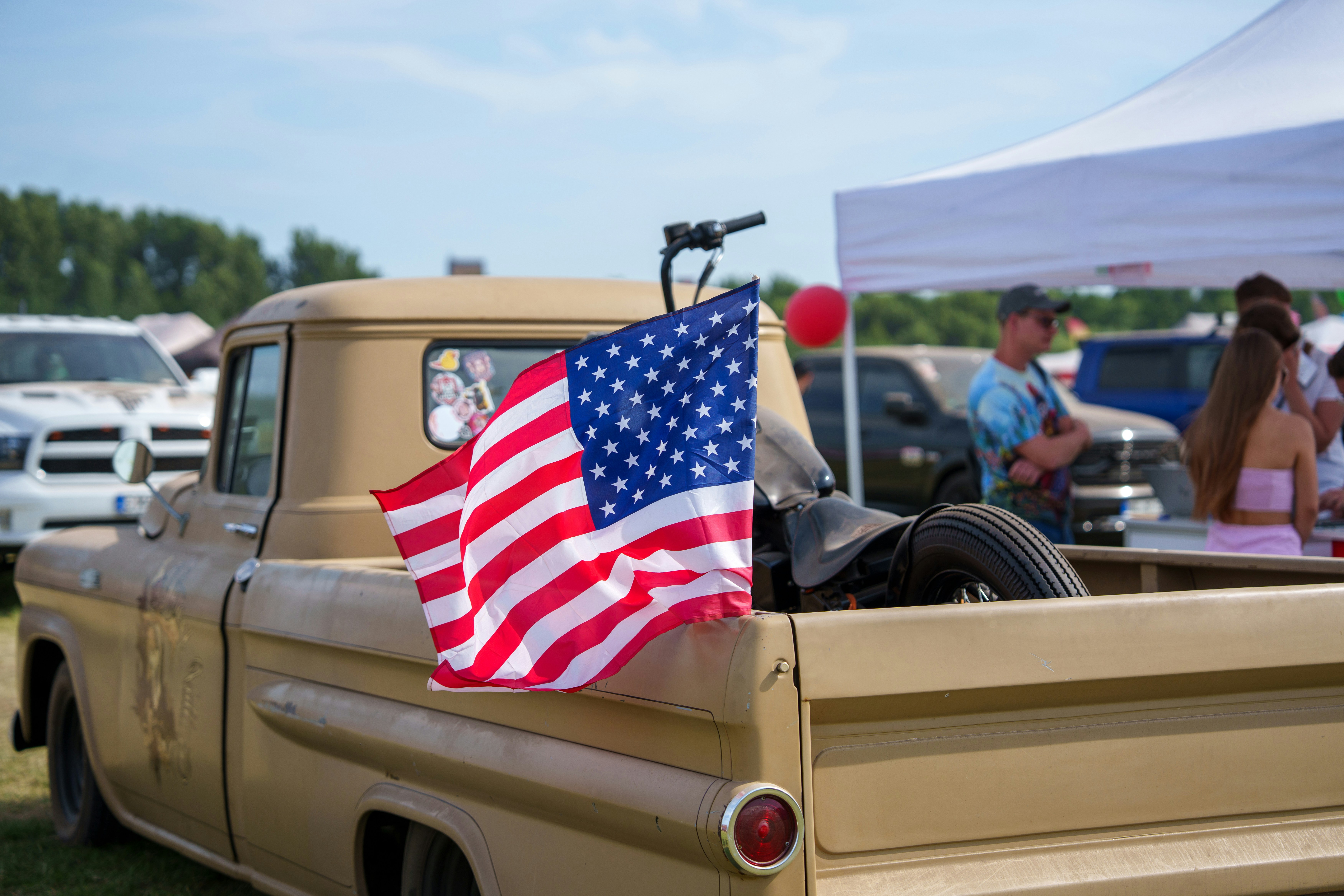 American Flag Draped Over a Vintage Pickup at a Summer Car Show