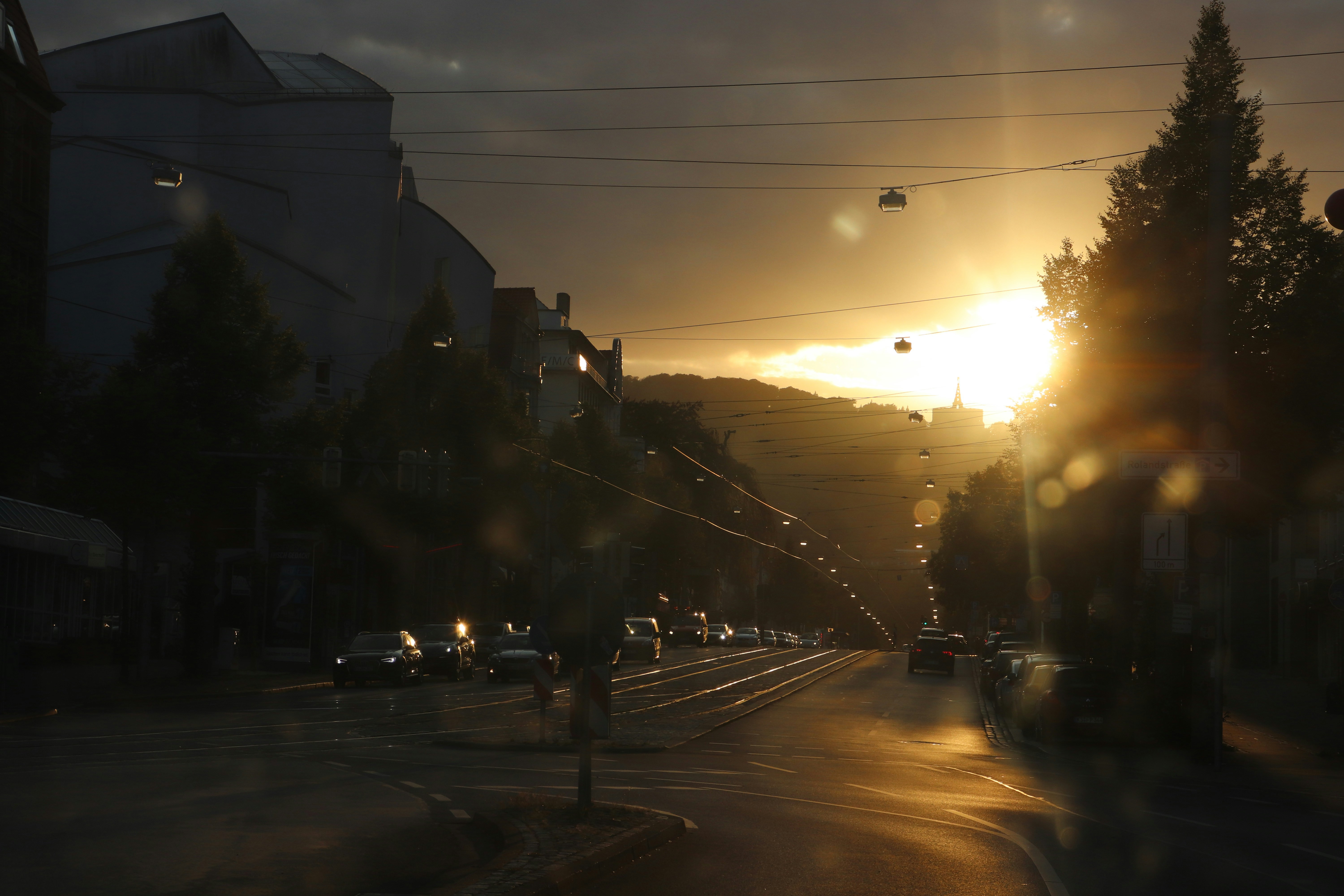 Sunlit boulevard at golden hour with tram cables and silhouettes