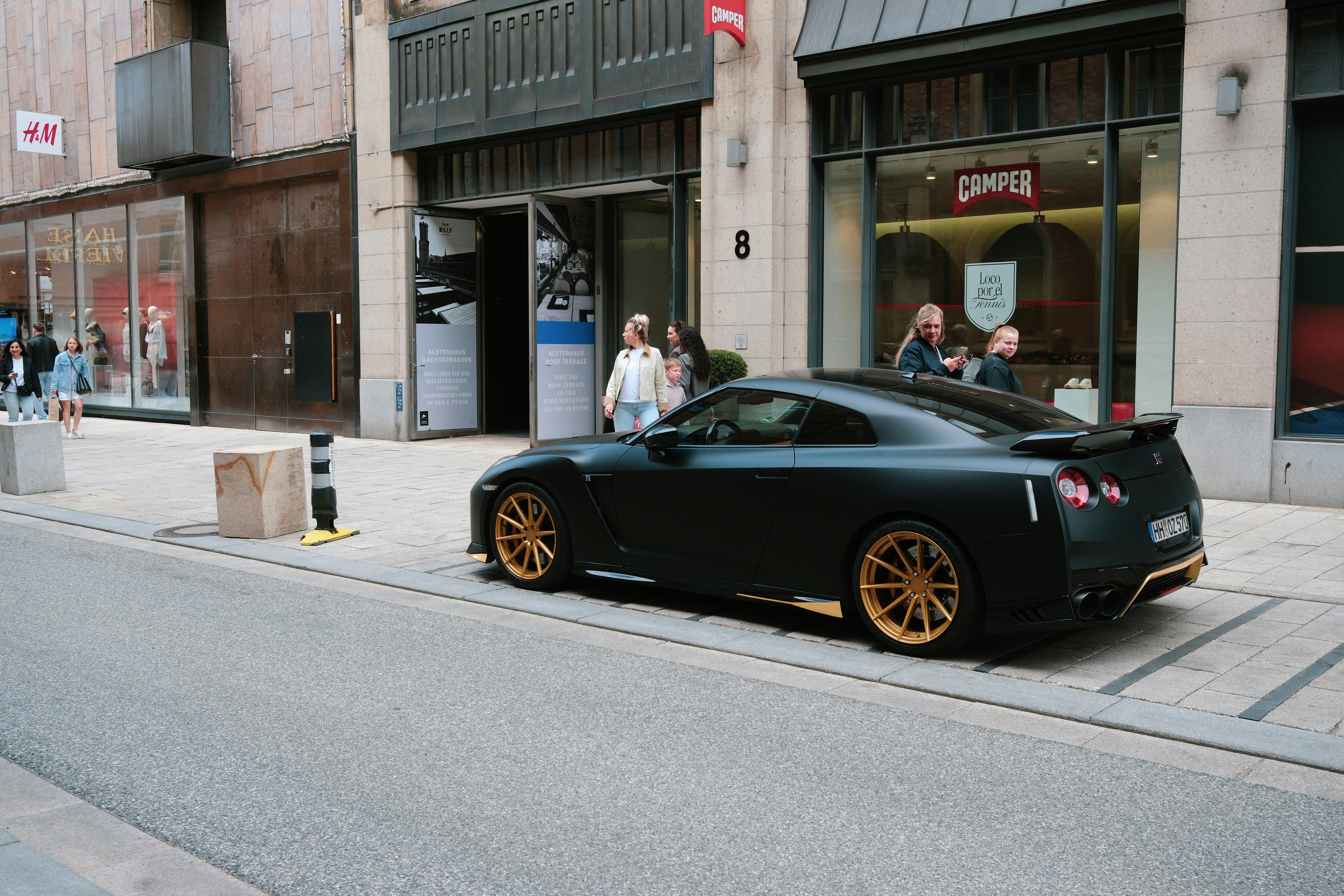 Matte black sports car with gold wheels anchors a stylish city street