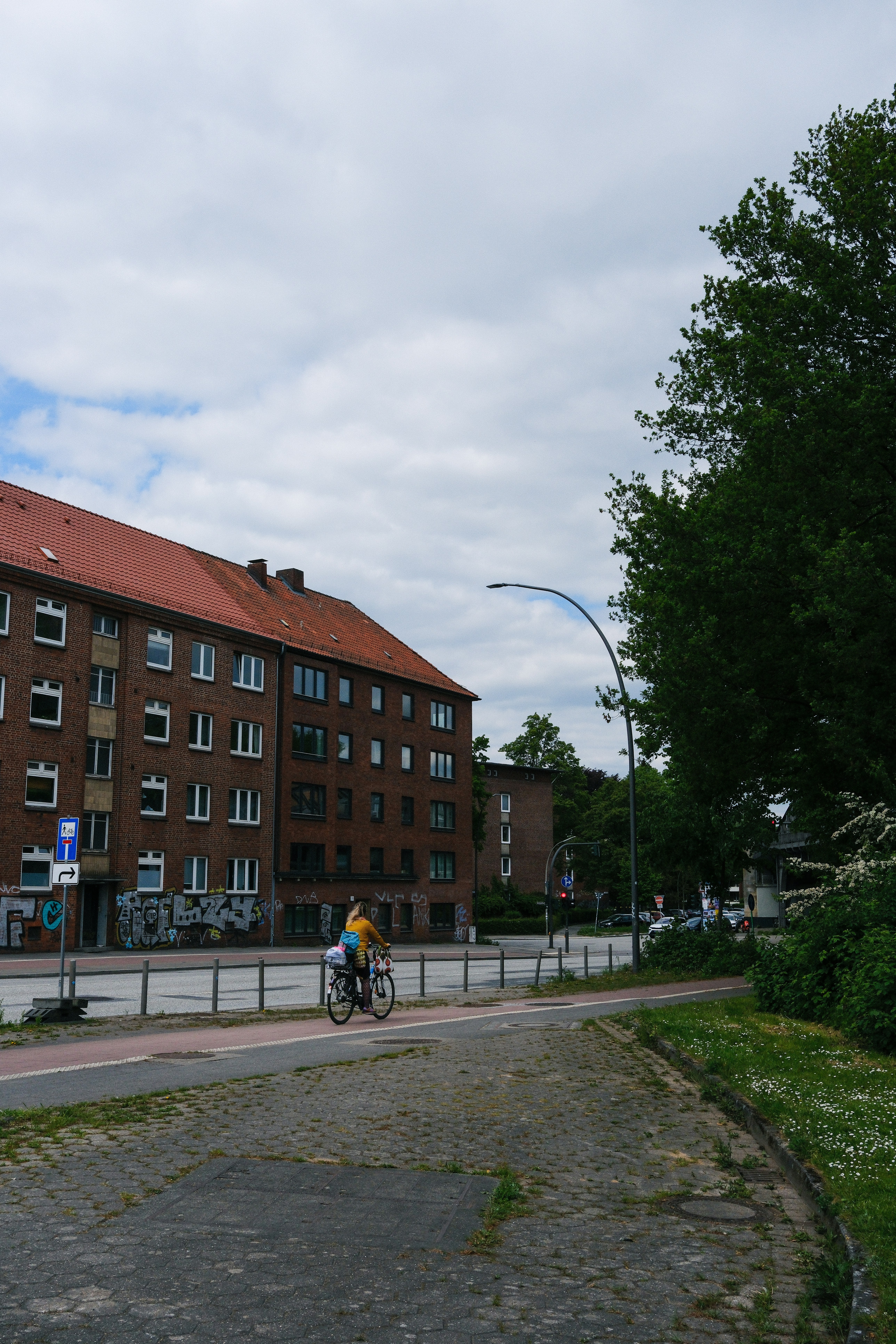 City Cyclists Under a Grey Sky by a Red Roofed Block