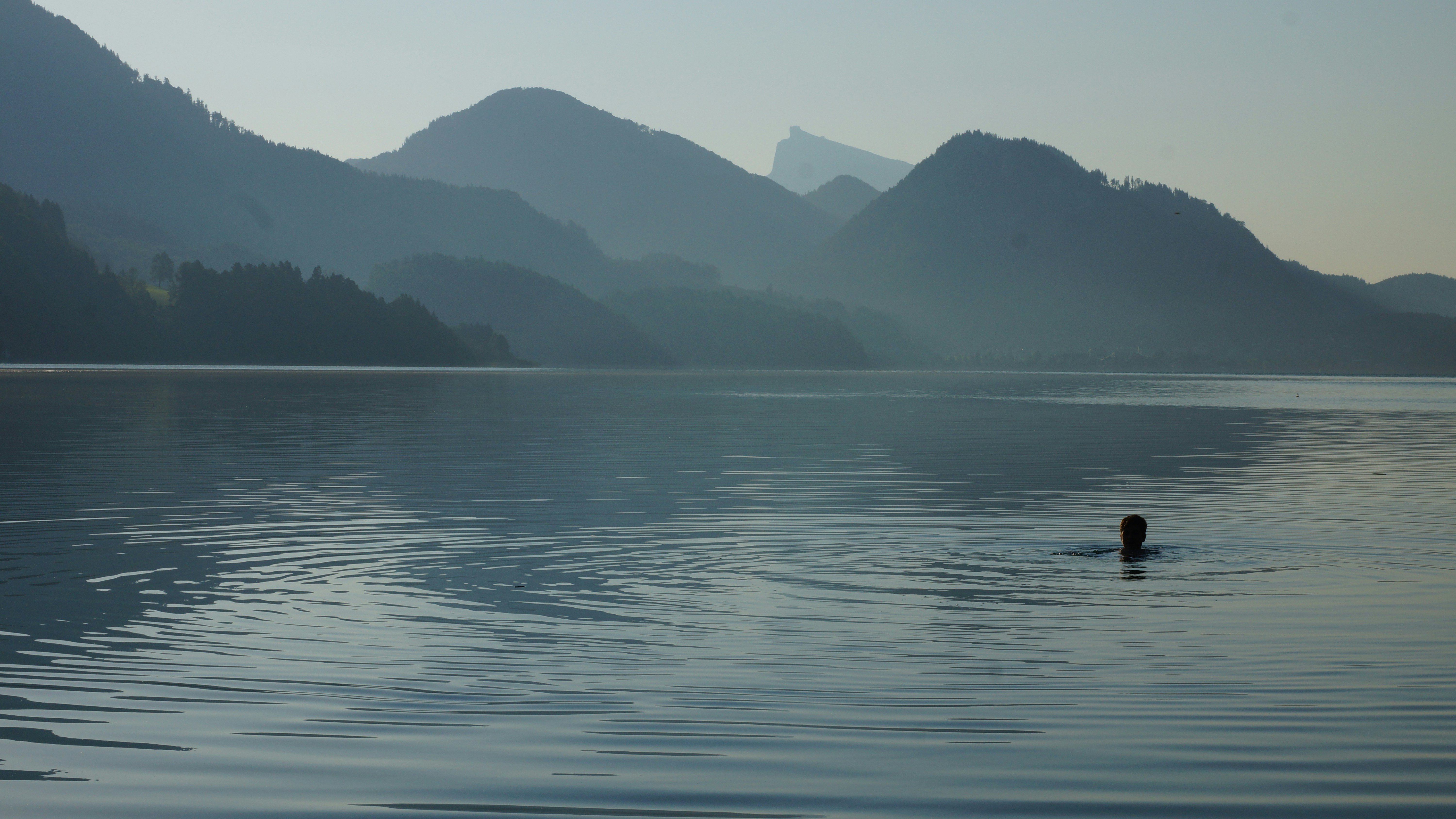 Misty Lake Portrait: solitary swimmer beneath layered peaks