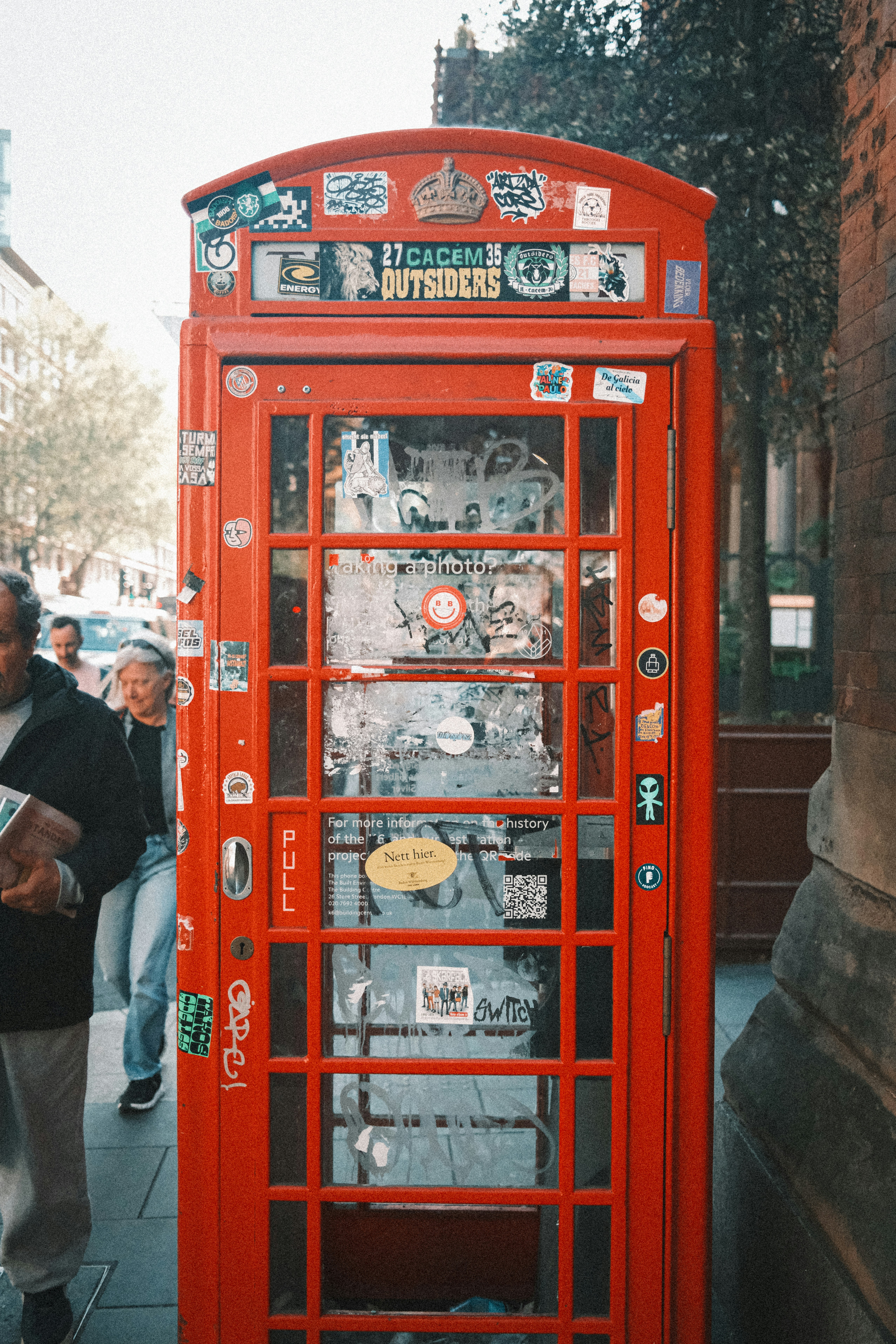 Crimson Kiosk: A Streetbound Red Telephone Booth Clad in Stickers