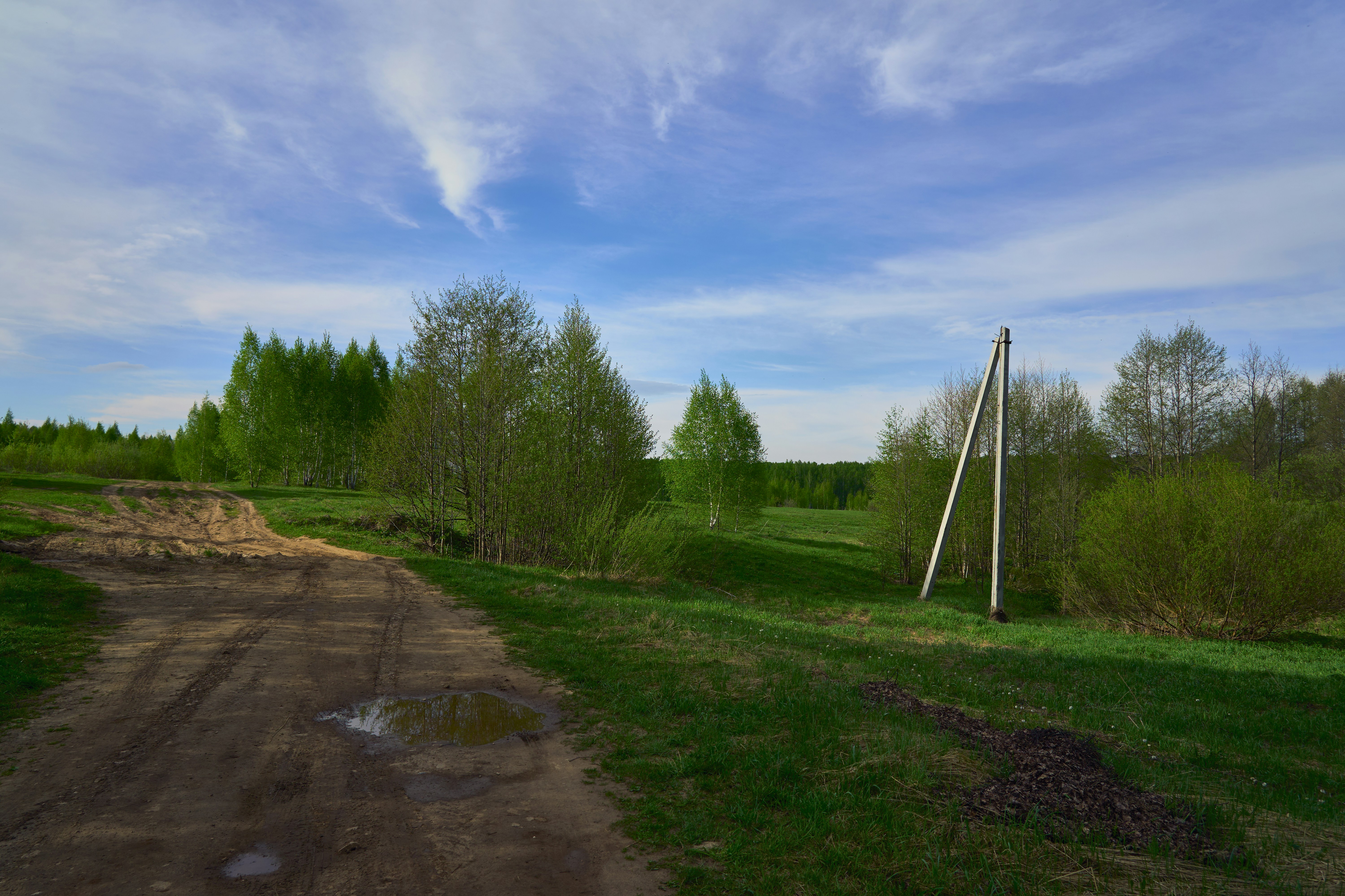 Dusty rural road and leaning utility pole under a blue sky