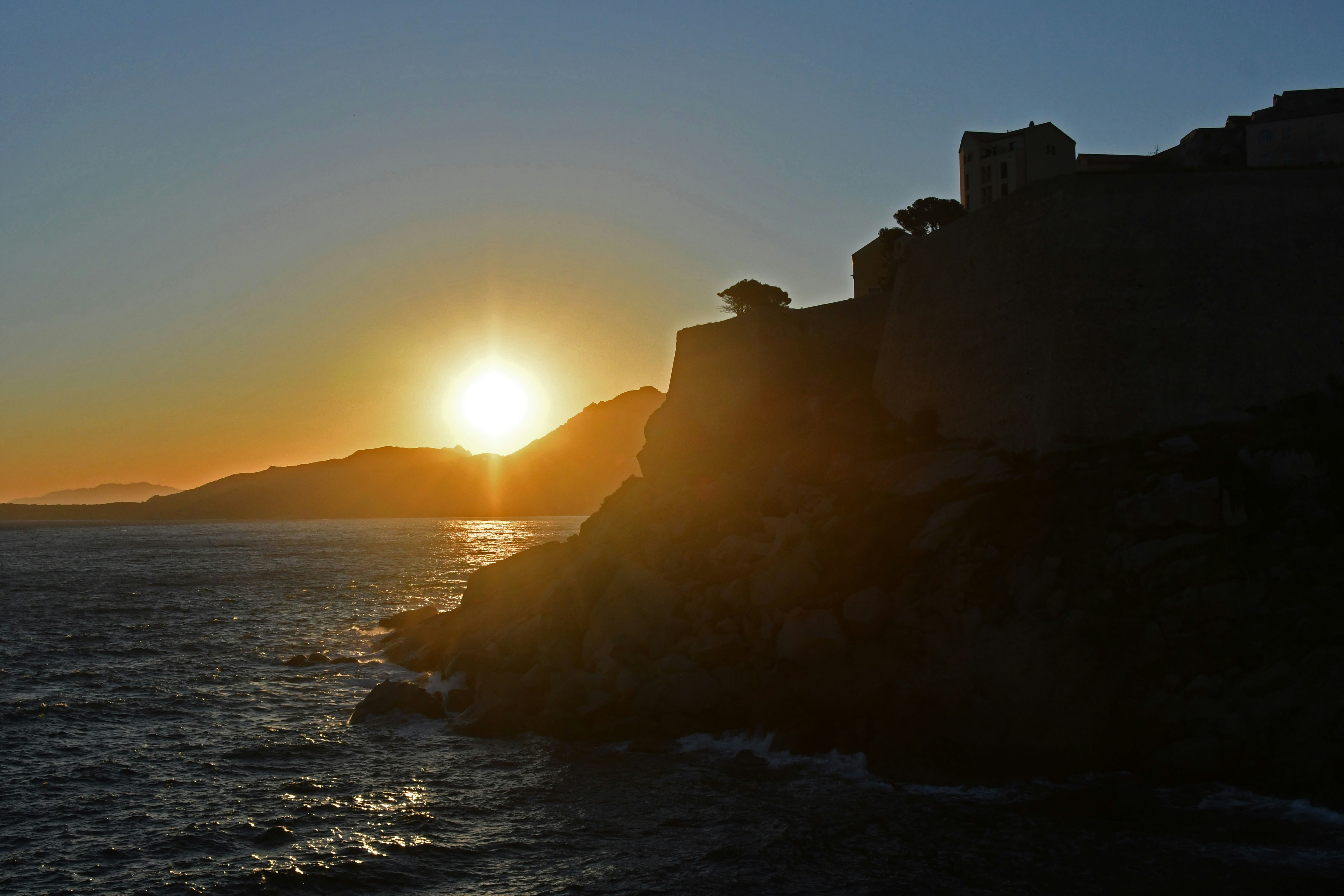 Sunlit cliff silhouette at sea with distant sunset