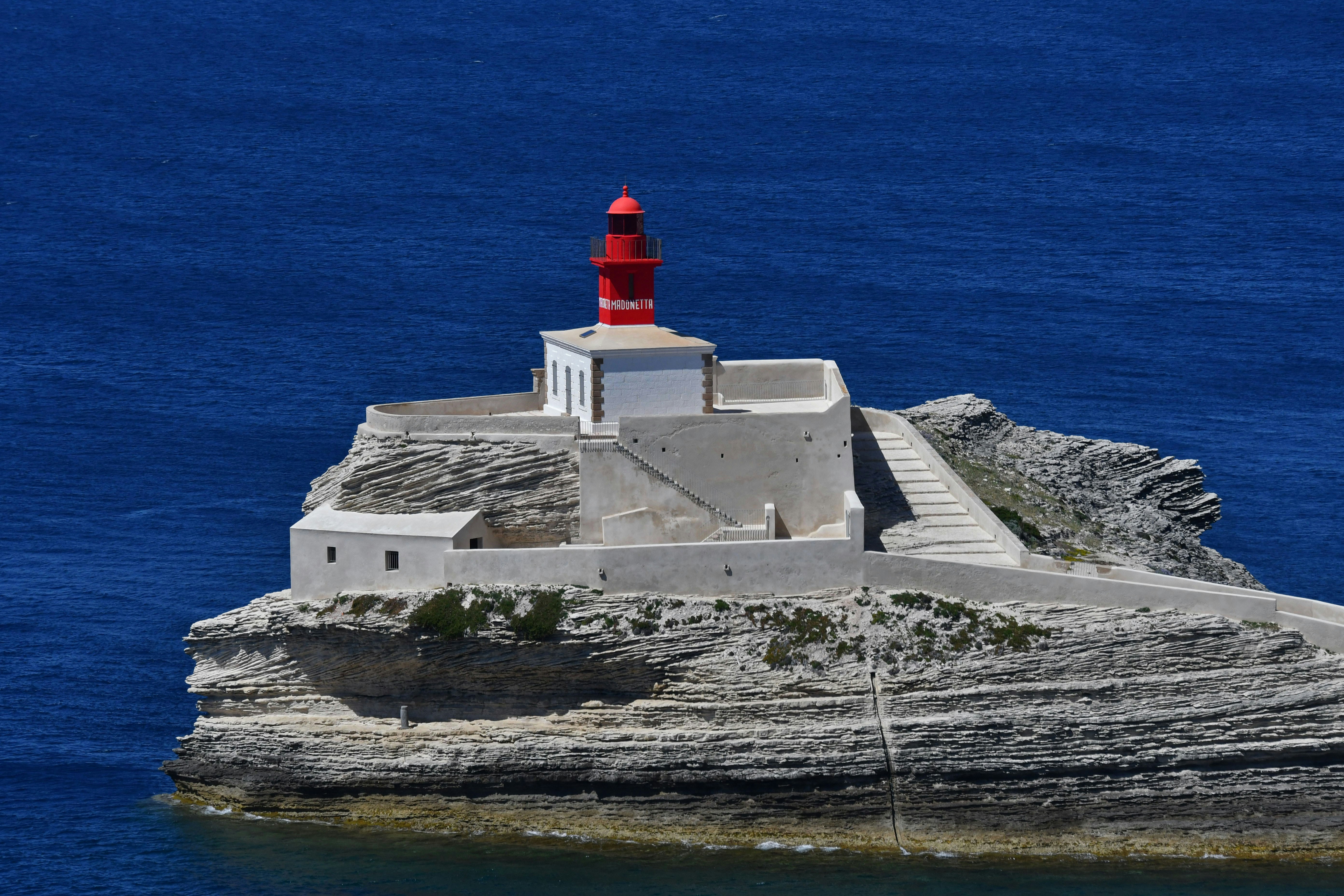 Red beacon on a sea-locked fortress: a lone lighthouse on basalt cliffs