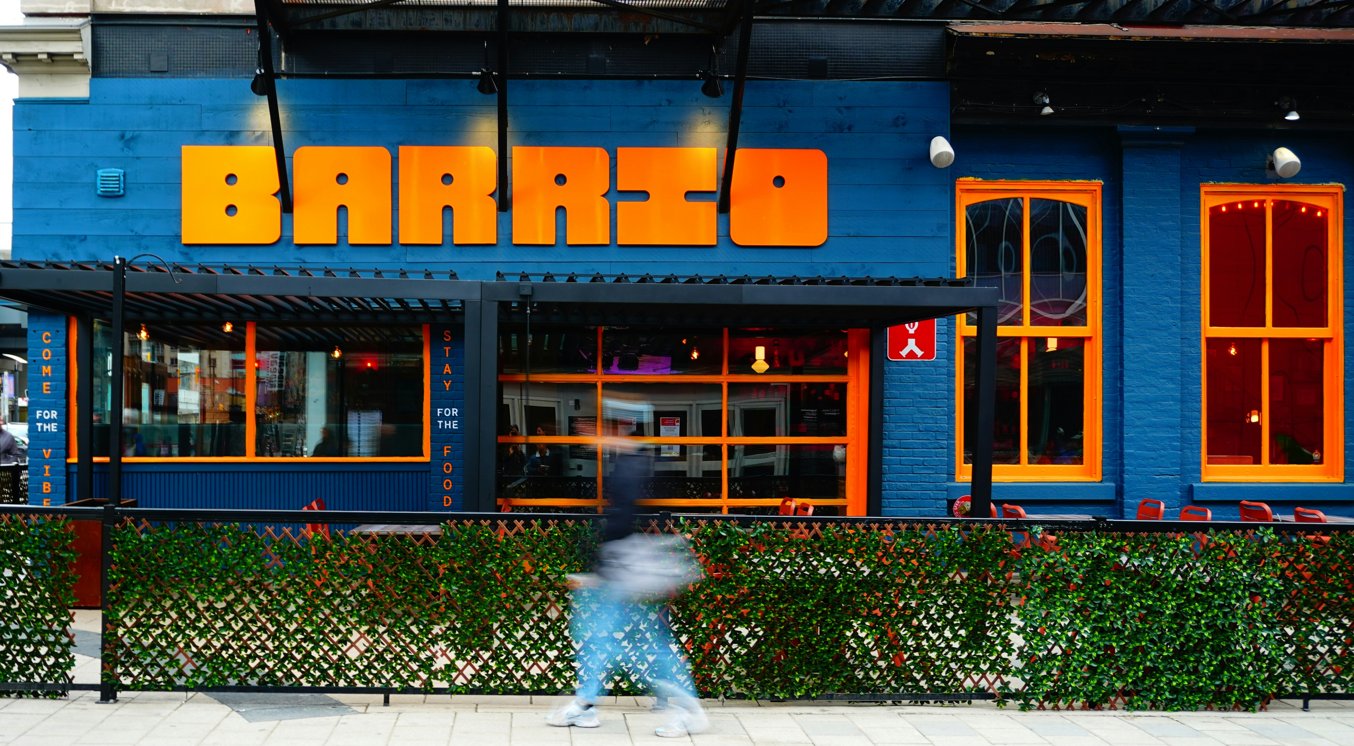 Bright Blue Facade of Barrio: Pedestrian Blur Under Vivid Orange Sign