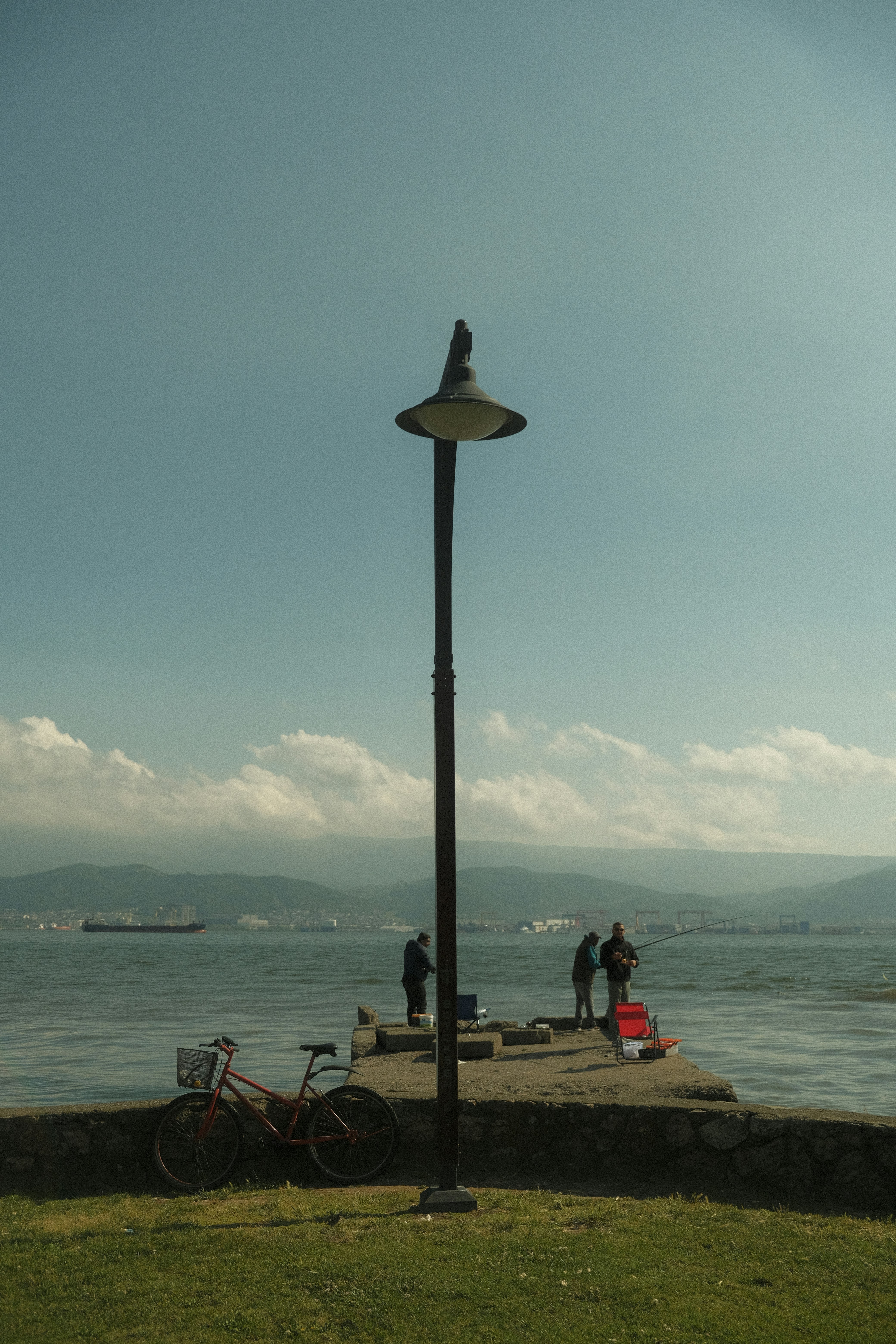 Harbor Evening: A lone lamppost on a quiet jetty with distant fishermen