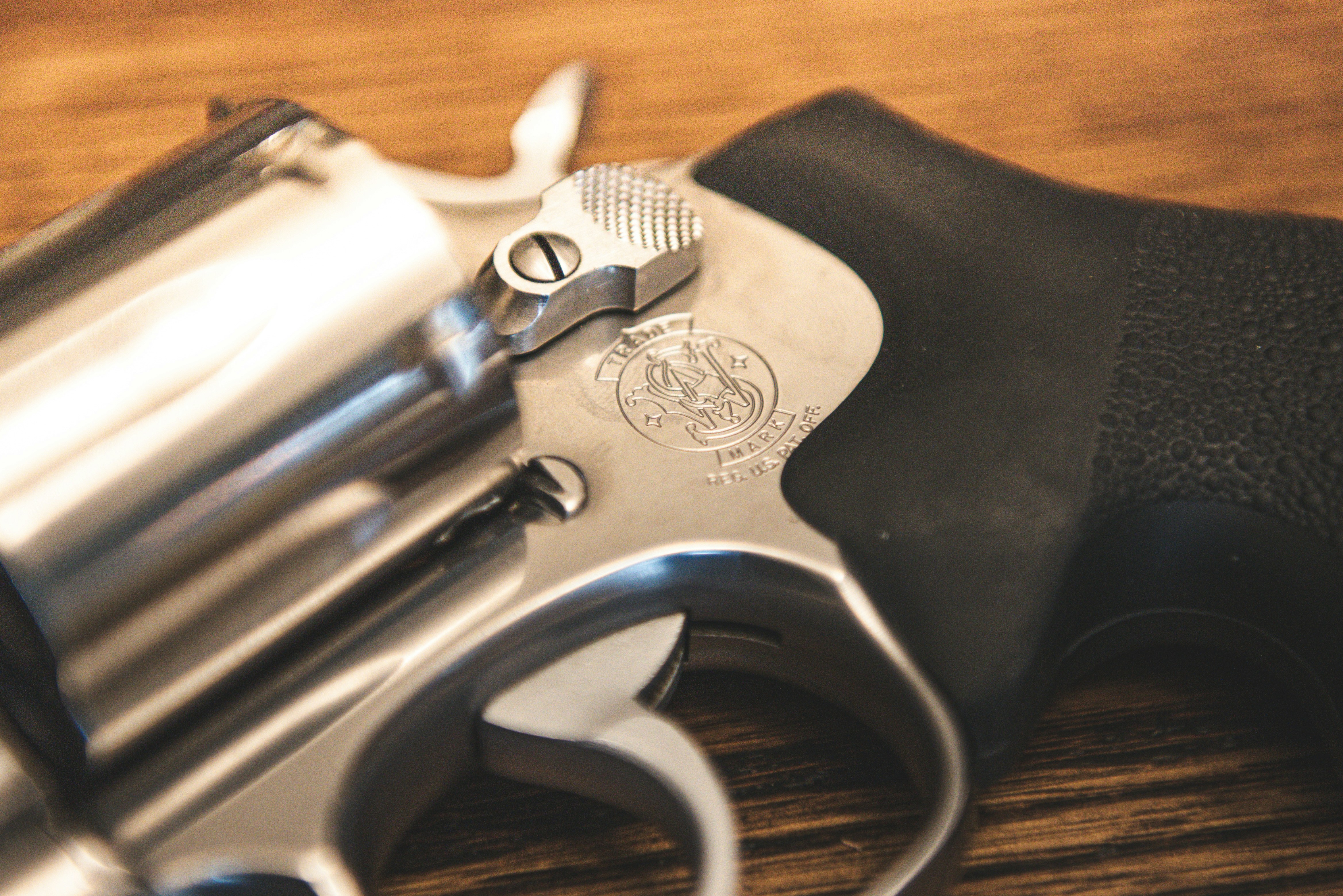 Stainless steel revolver with black grip and wooden background.