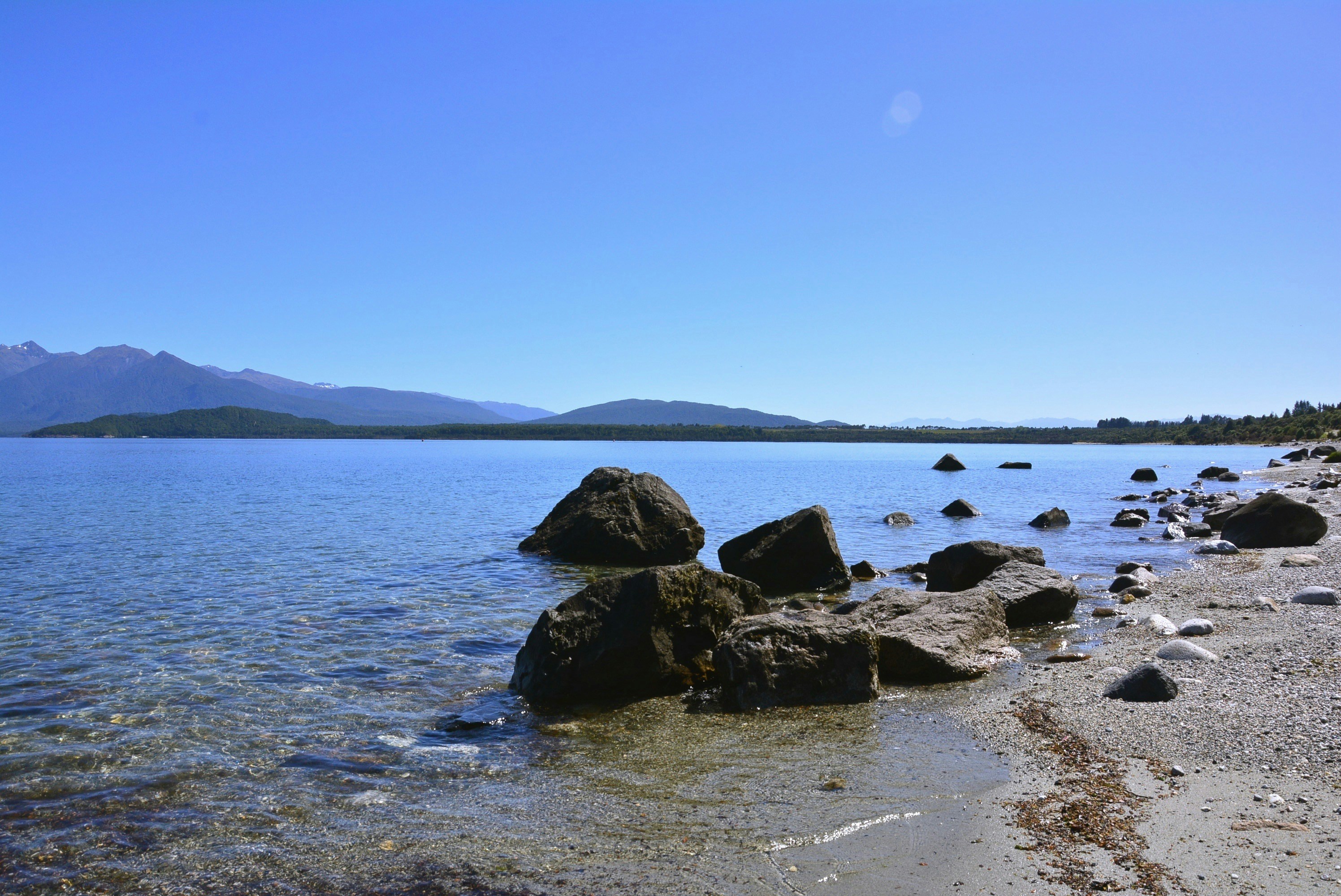 Shoreline Stillness: Boulders Waiting at the Lake’s Edge Under a Clear Sky