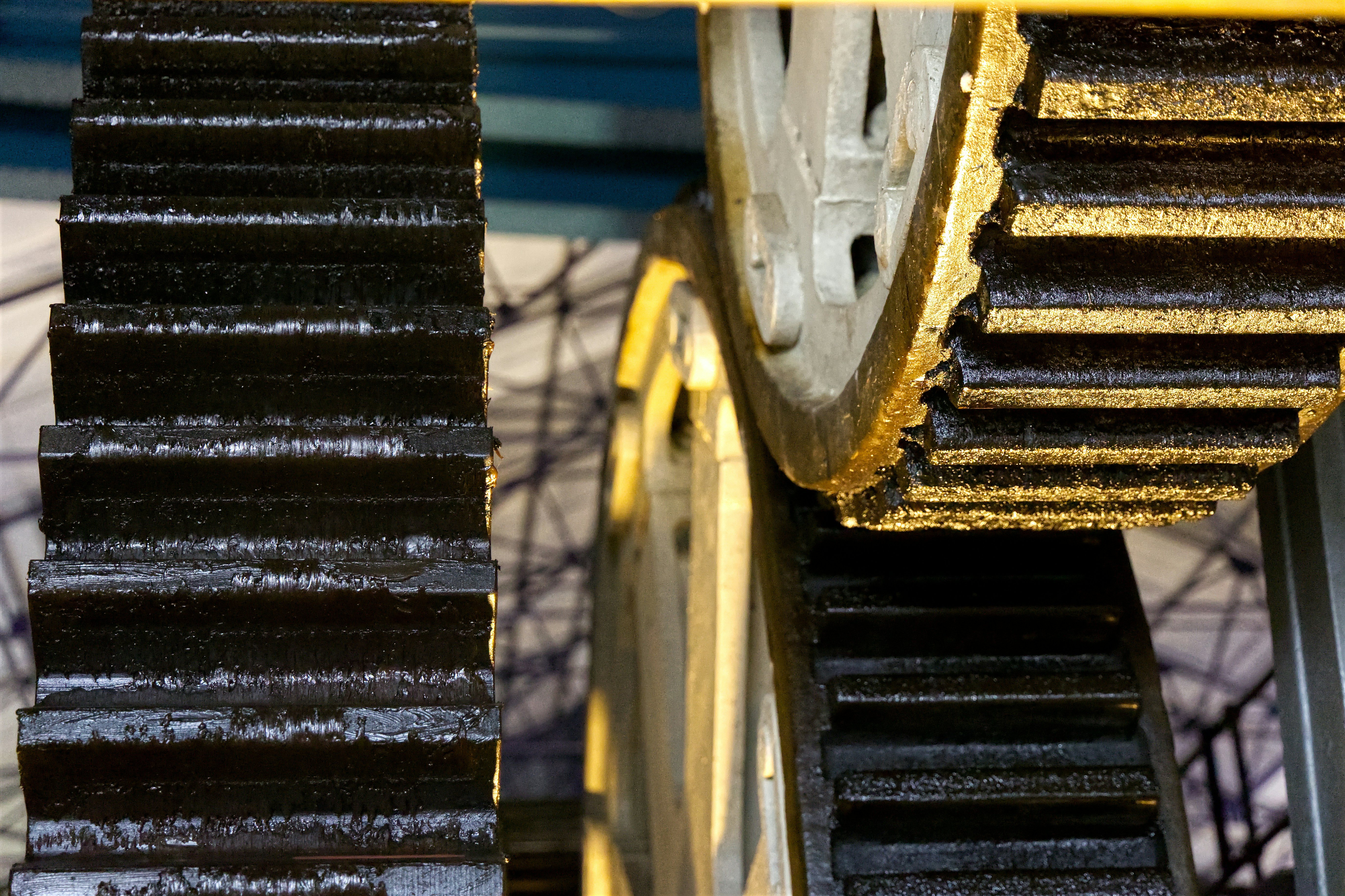 Close-up of intermeshing cogwheels with dark metallic teeth and a hint of gold-tinted highlights, revealing texture and mechanical depth.