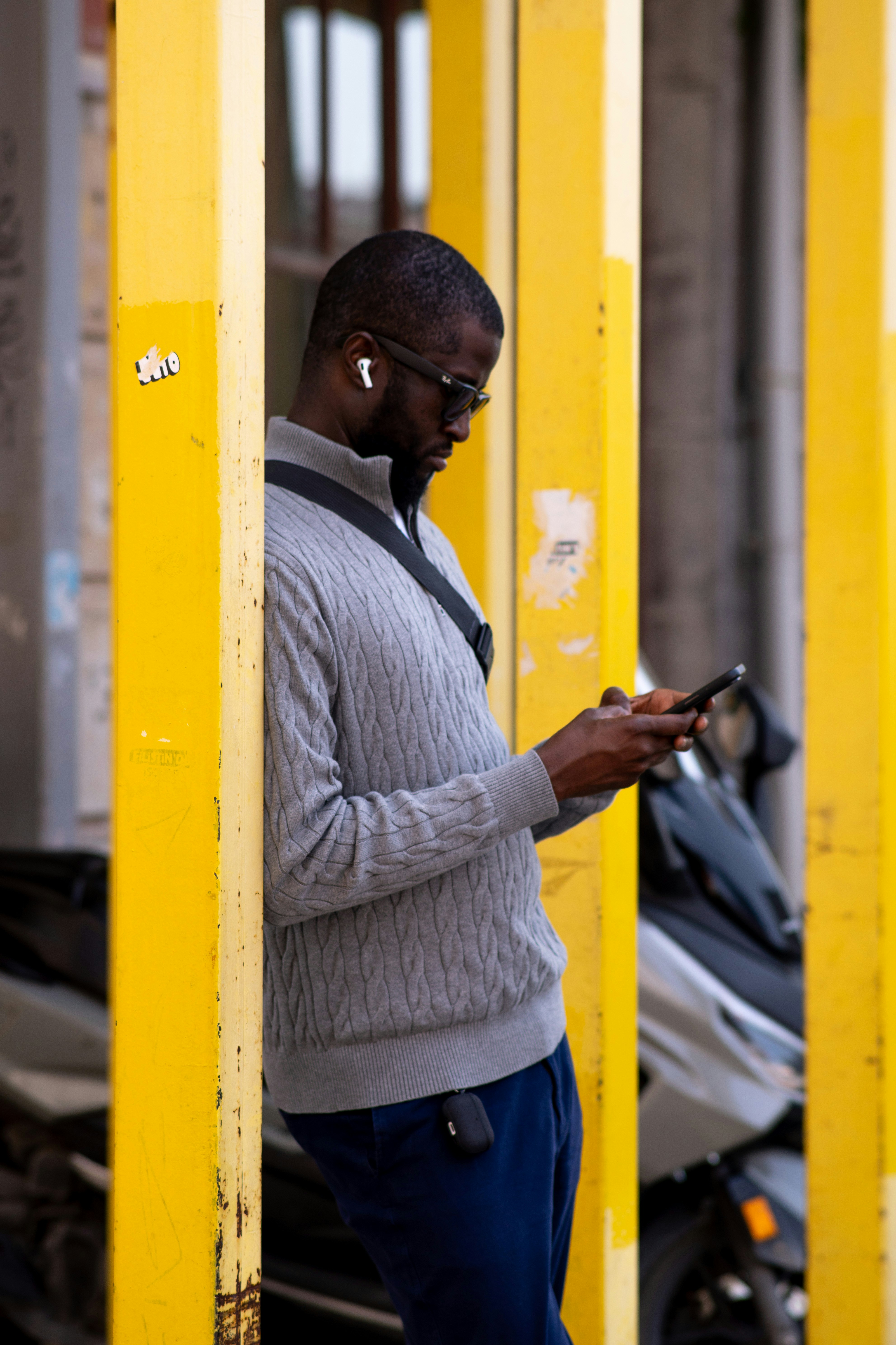 Focused Pause: A man in a gray knit sweater glances at his phone between bright yellow columns
