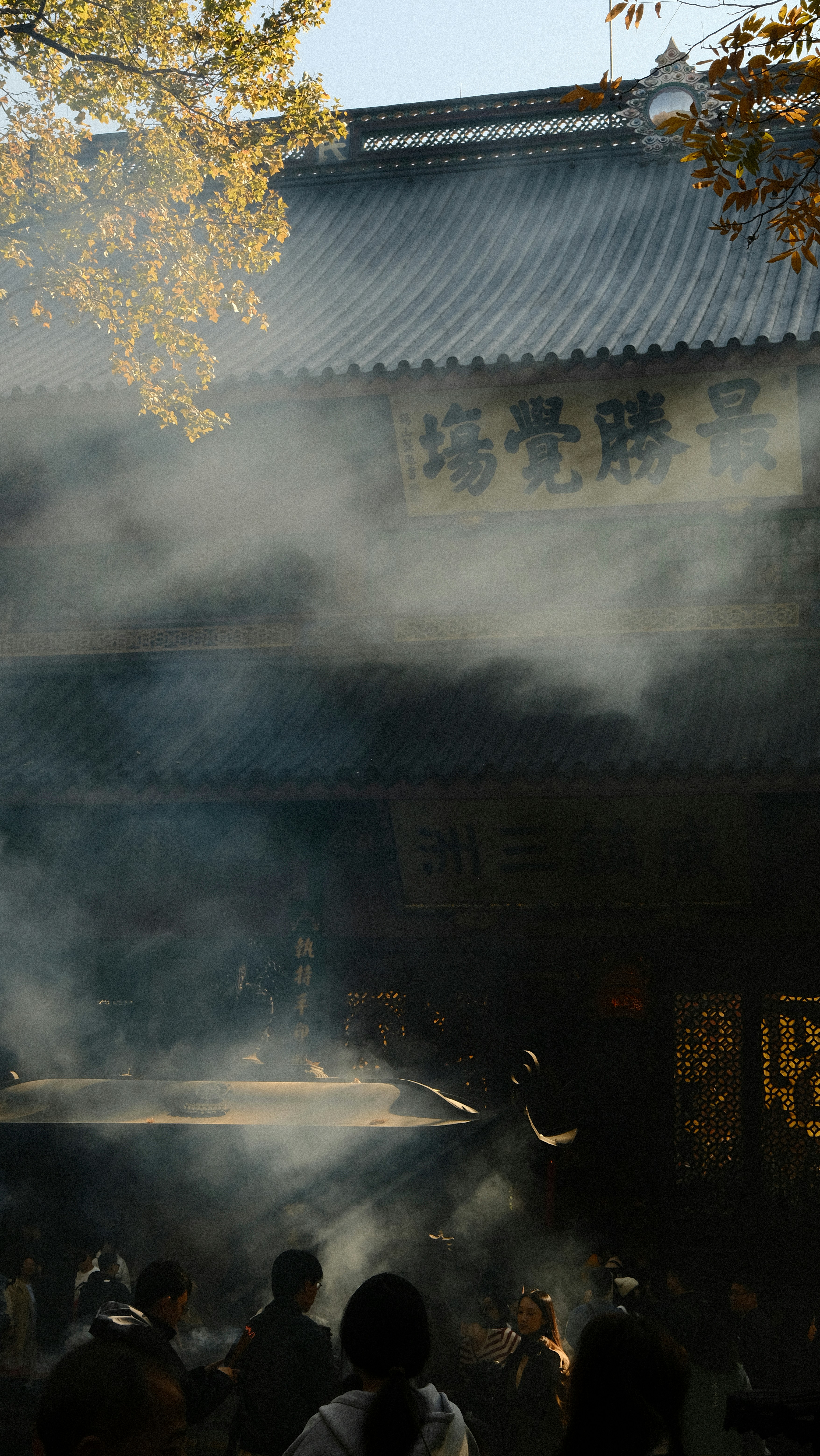 Smoke and Sacred Facade: A Glimpse of Temple Entrance Beneath Autumn Canopy