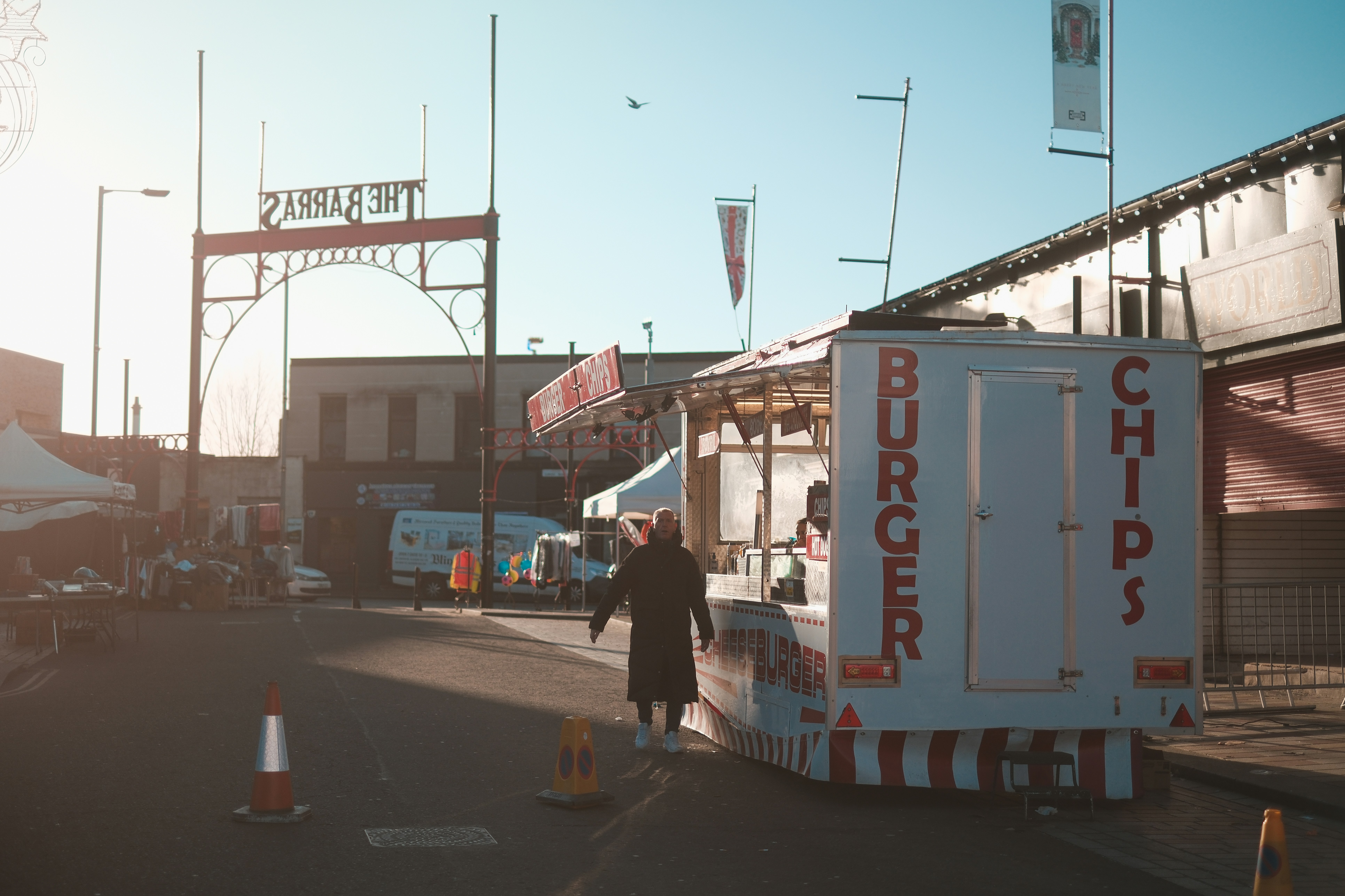 Sunlit Streetfront: A Food Stall and a Shadowed Figure at The Market Gate