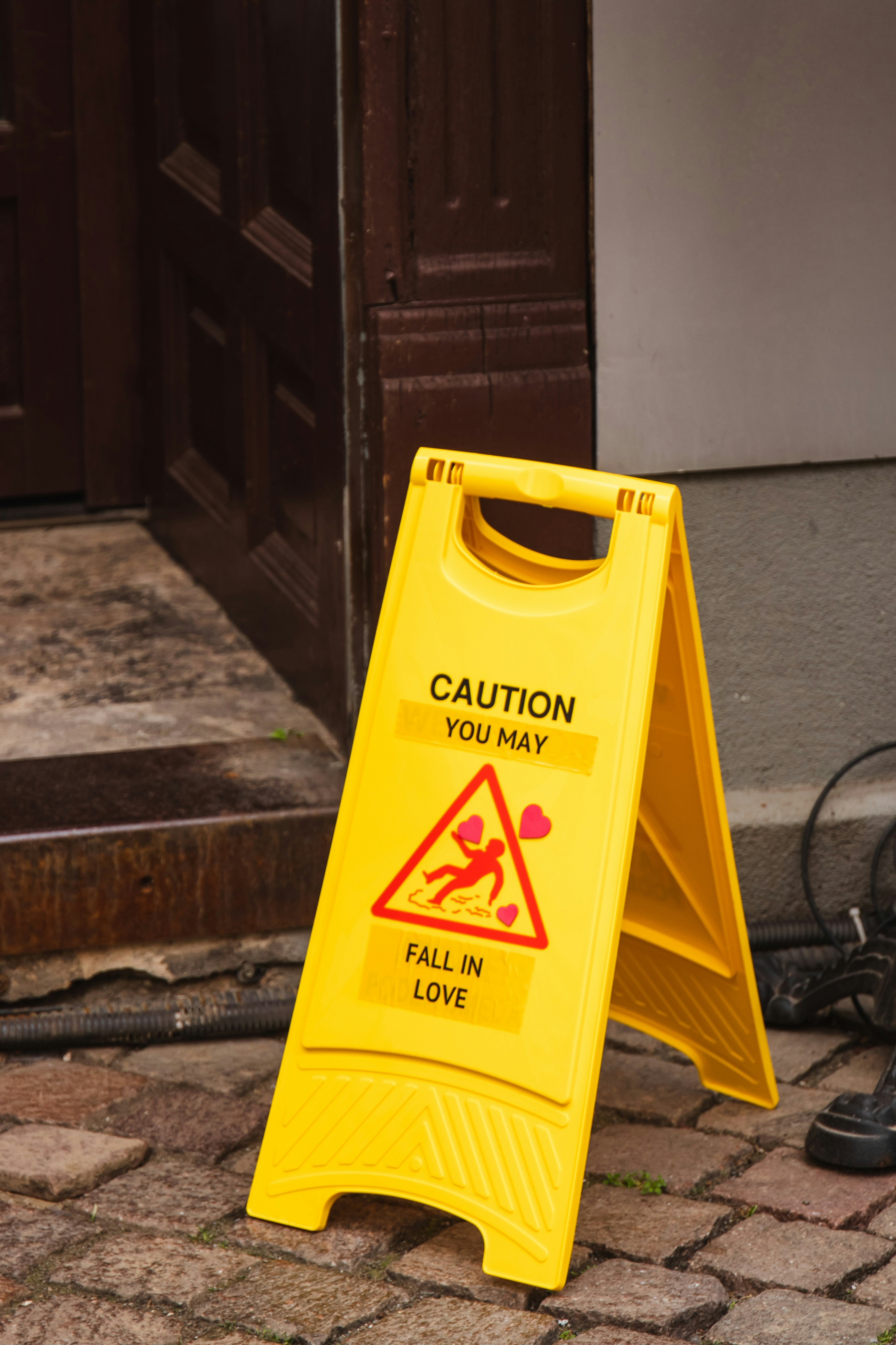 Caution in the Corner: A Bright Solo Sign Against a Quiet Cobblestone Threshold