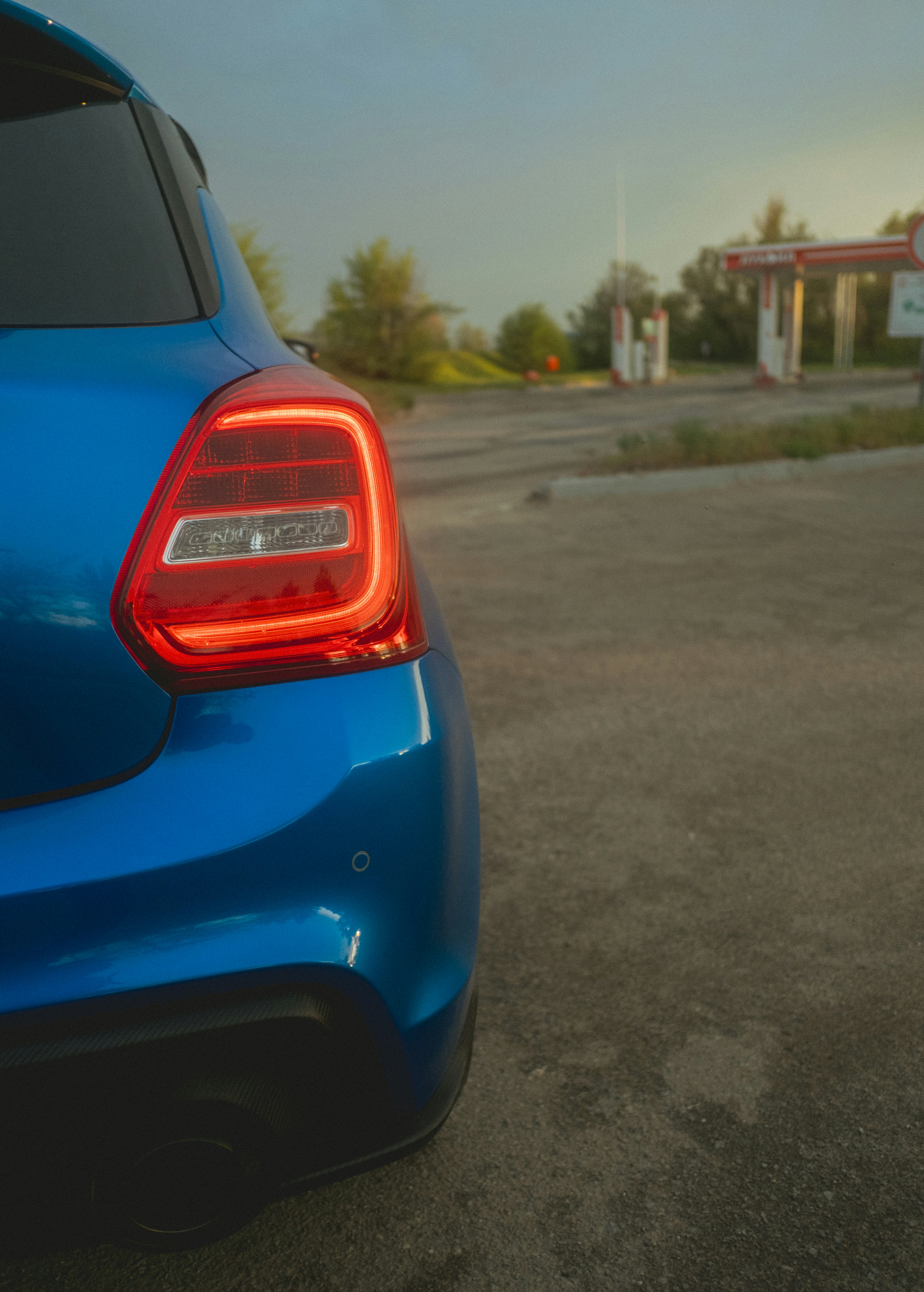 Blue hatchback tail light in focus against a late-afternoon depot
