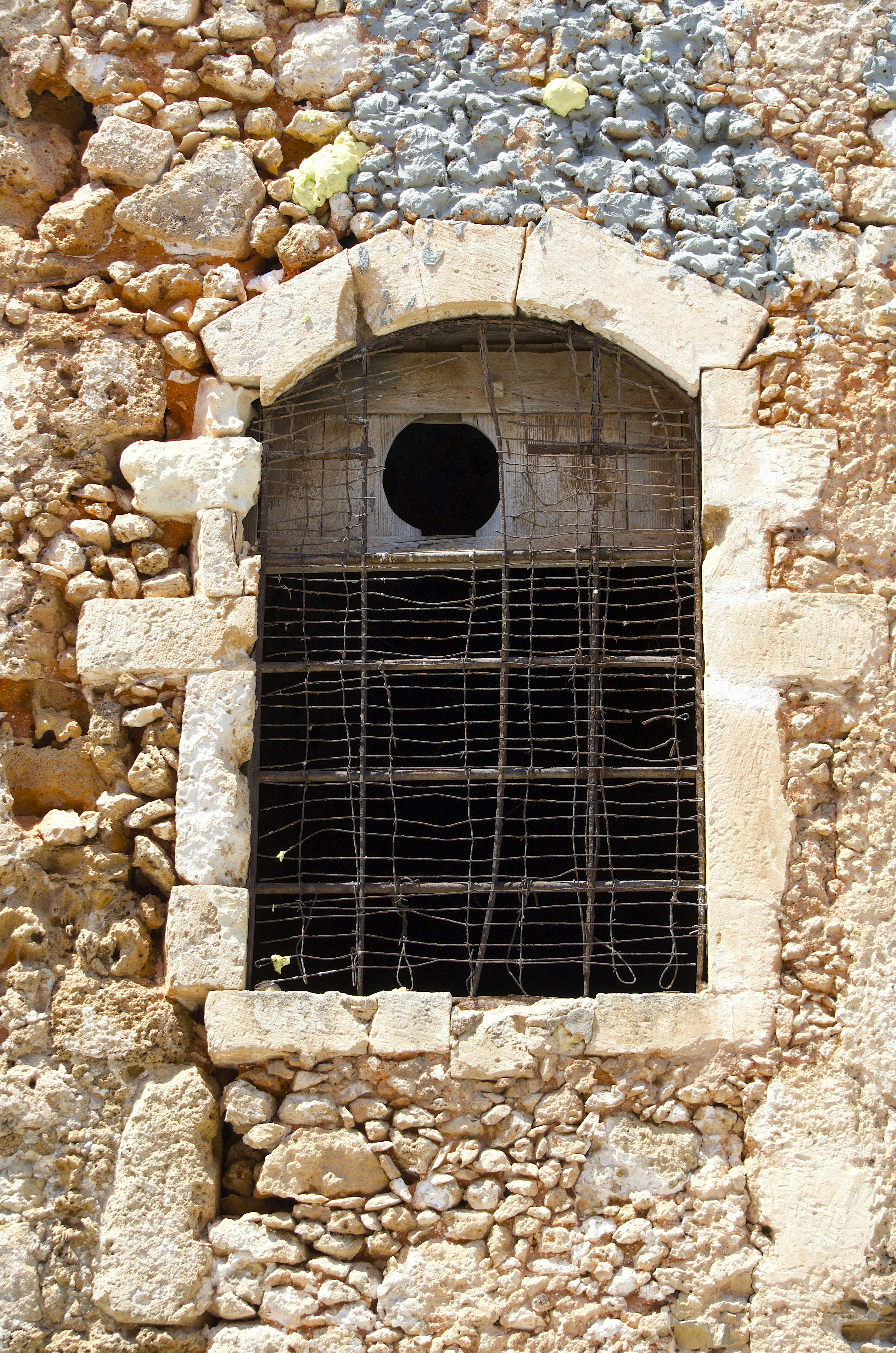 Weathered Archway with Iron Grille: A stone window in a sunlit ruin