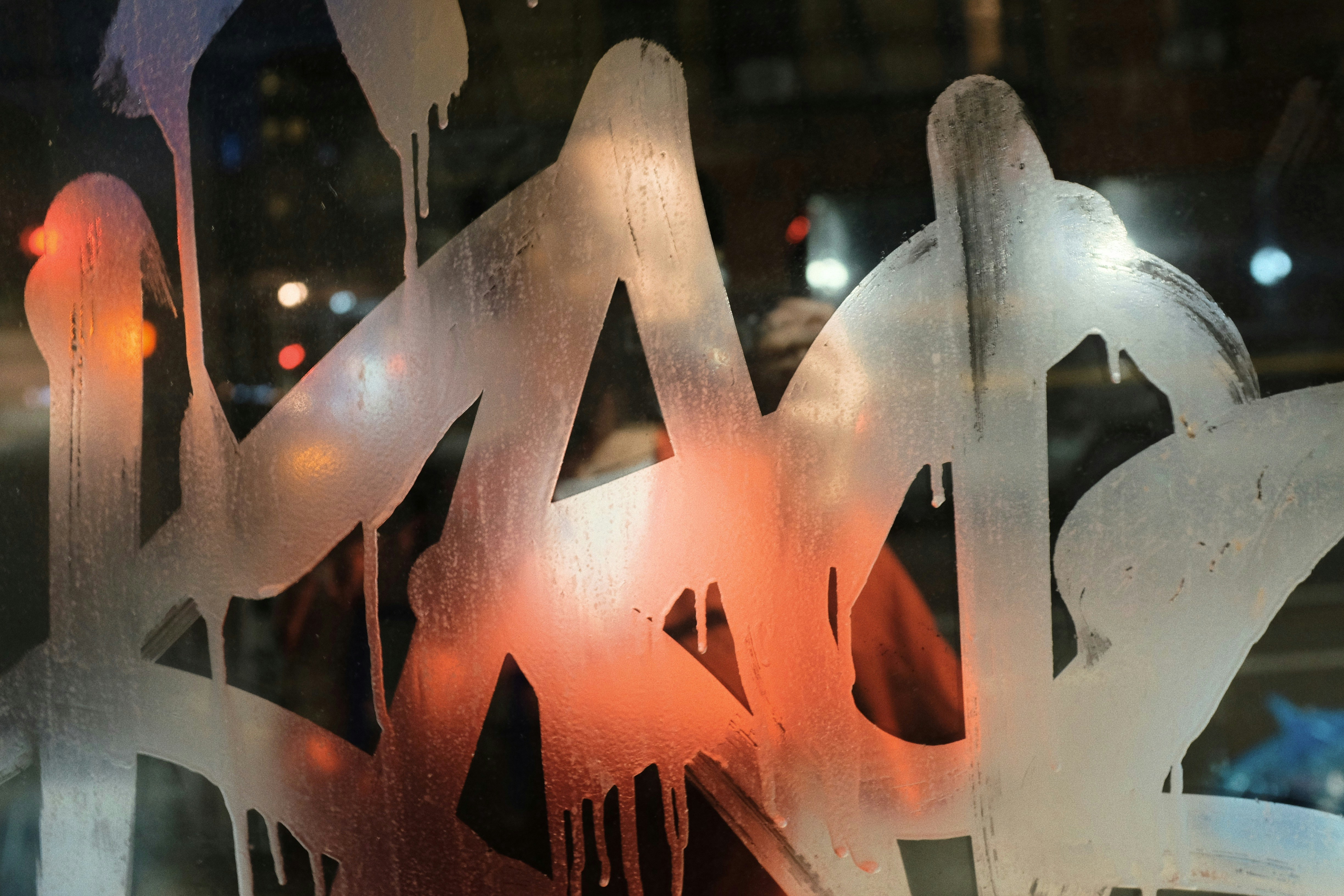 Frosty glass with bold graffiti and warm city lights peeking through, creating a moody urban abstraction.
