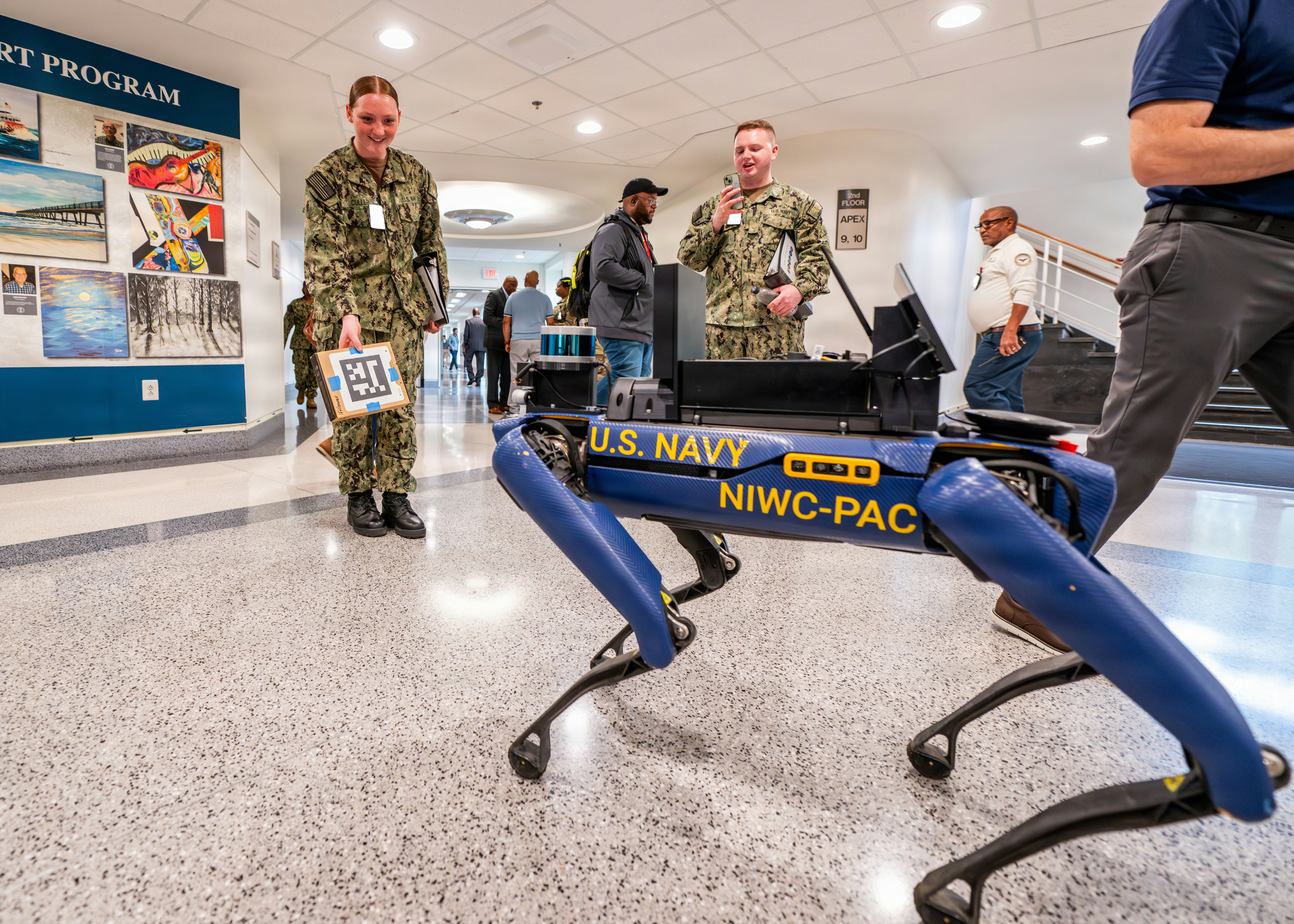 U.S. Navy Hospital Corpsman Seaman Madisen Marie Culler interacts with “Maverick,” a Collaborative Helper Autonomous Shipboard Exploration Robot, or CHASER, during the Department of War’s annual Lab Day at the Pentagon in Arlington, Virginia, May 6, 2026. The robot has sensors and software developed by the Naval Information Warfare Center Pacific that enable 3D mapping of the interior of a GPS-denied environment, such as a room, ship, or cave, and transmits that rendering to increase situational awareness. (U.S. Army photo by Bernardo Fuller) (This photo was altered for security purposes by blurring out identification badges.)