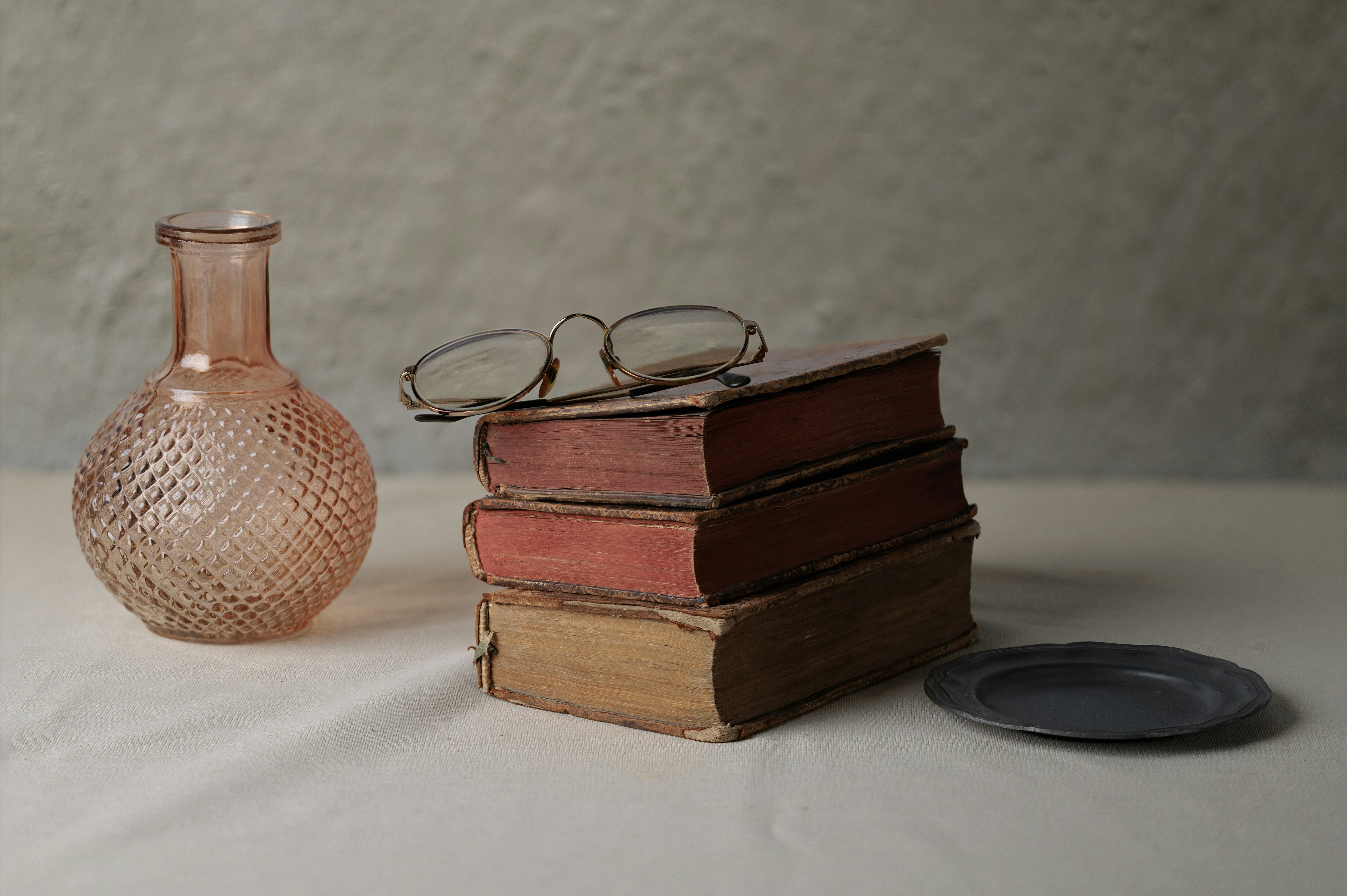 Stack of aged books and vintage glass with reading glasses resting on top