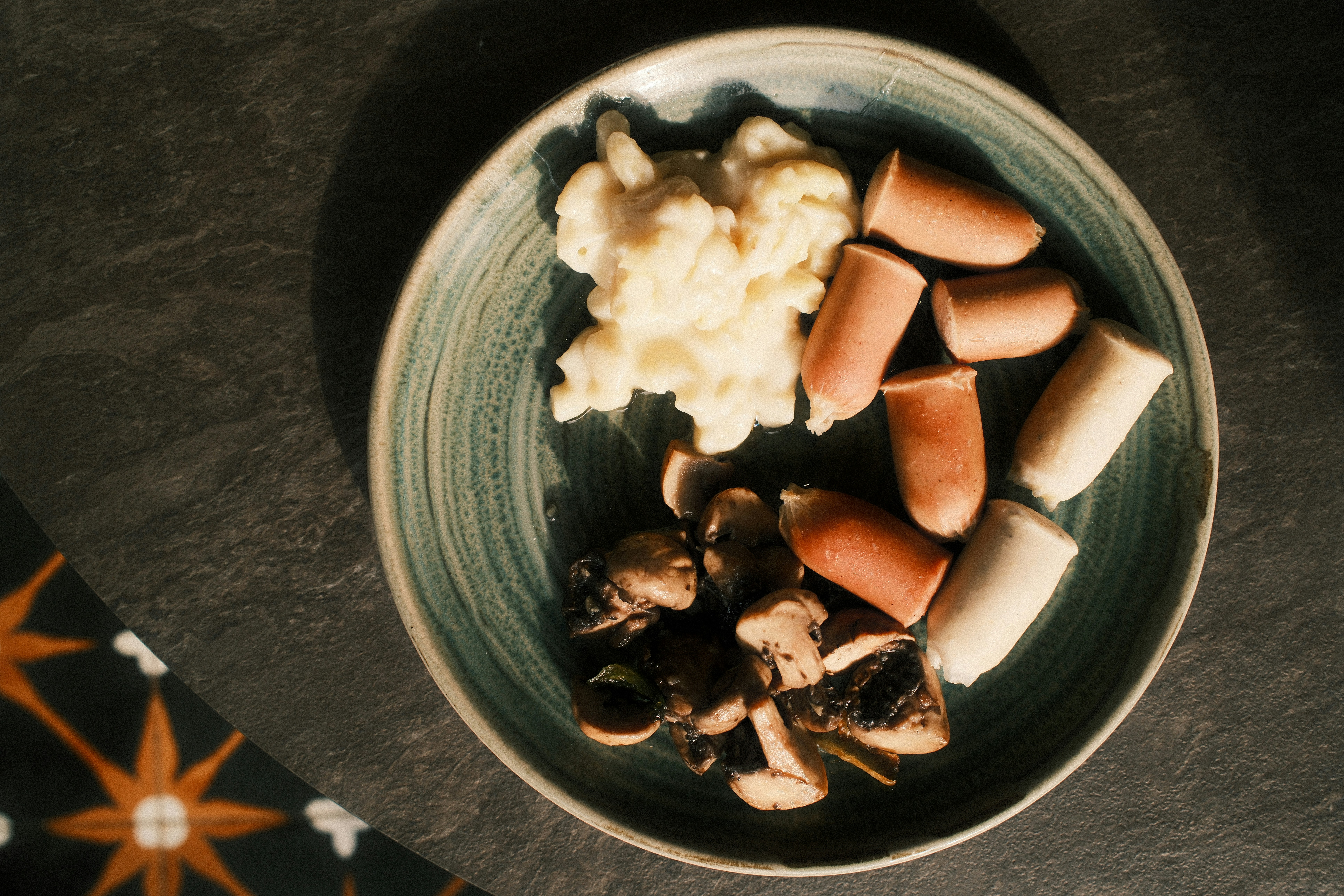 A plate with sausages, mushrooms, and mashed potatoes.
