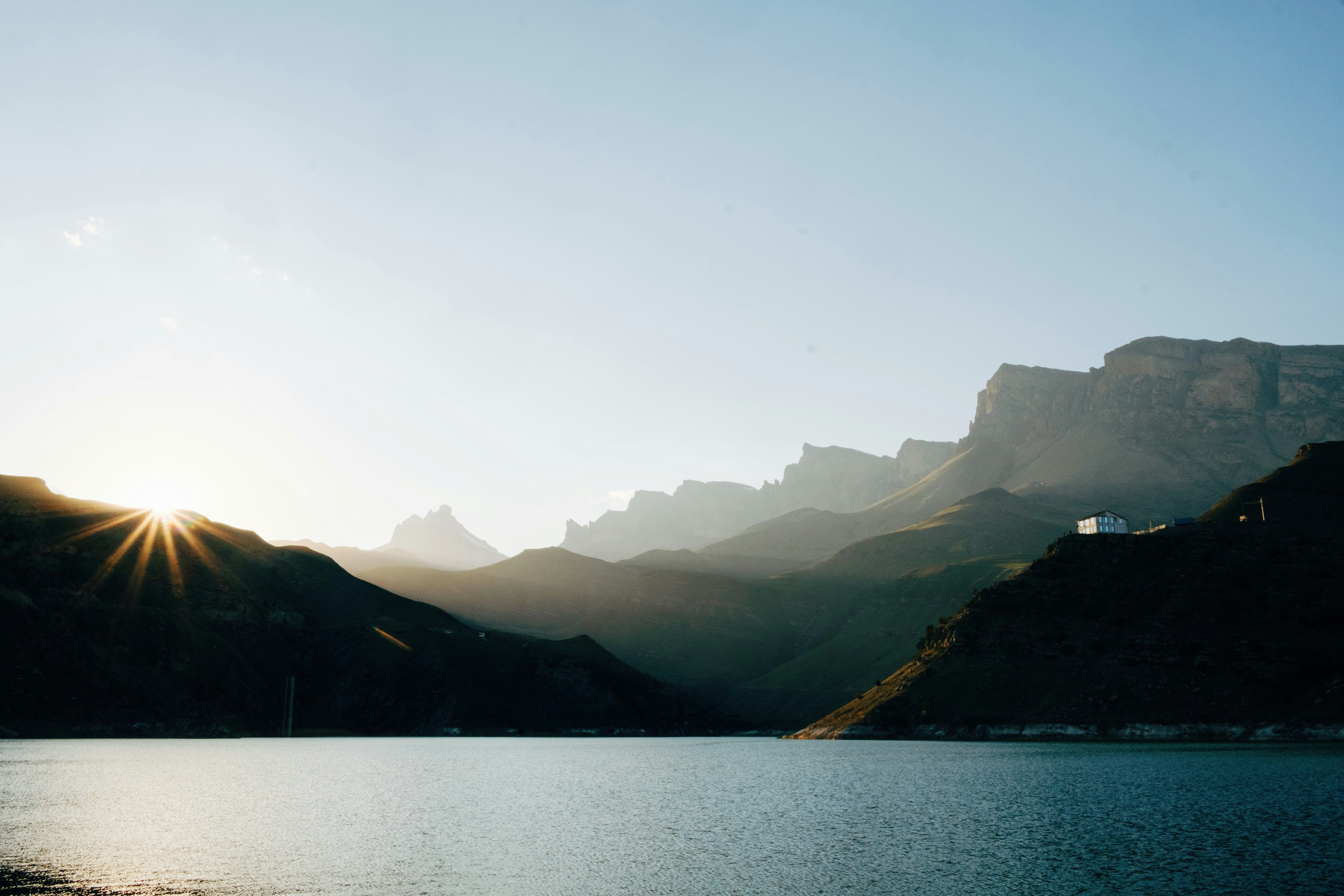Sunburst Over Alpine Fjord: Distant Peaks Meet Calm Waters
