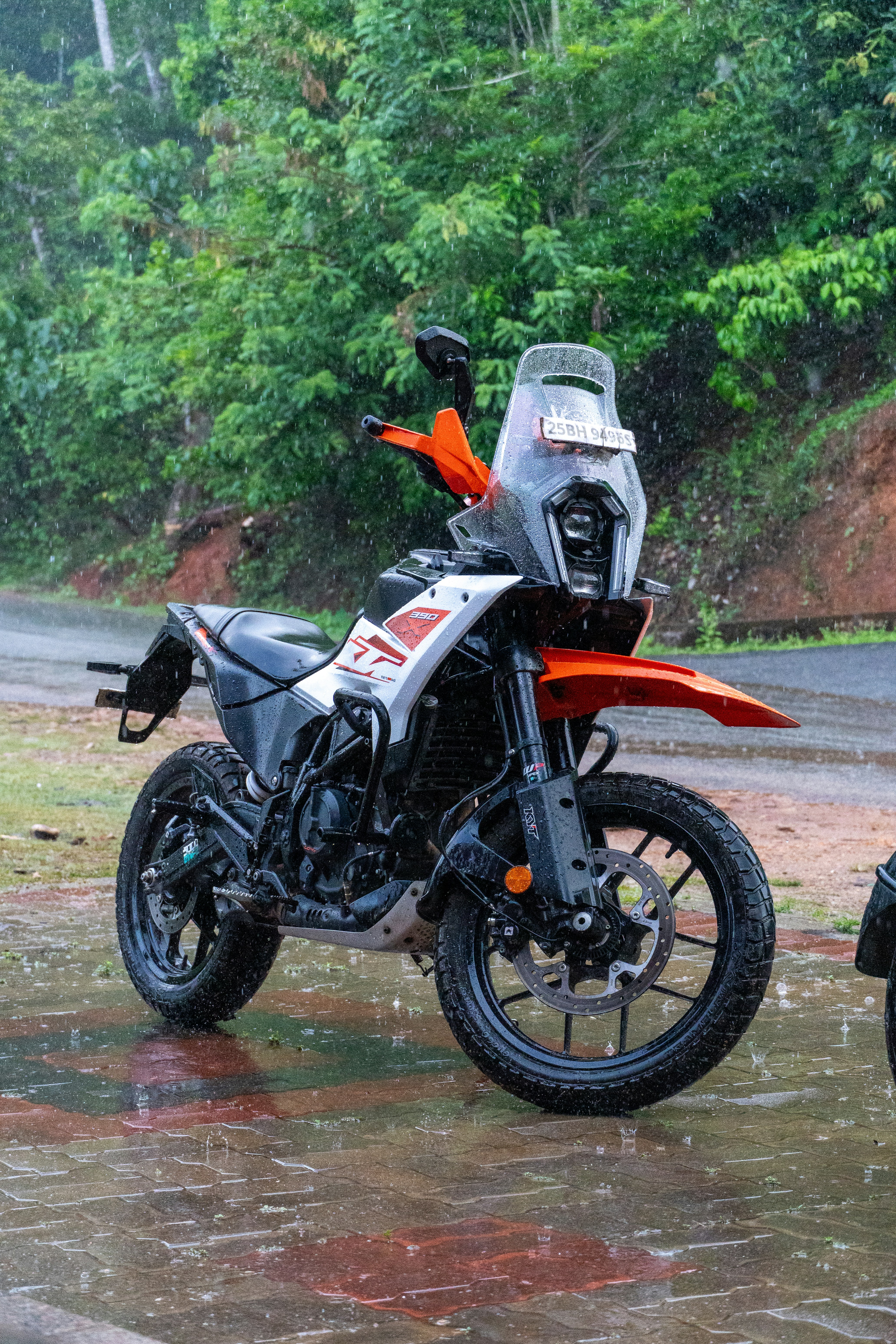 Orange and black adventure bike under light rain on a wet roadside