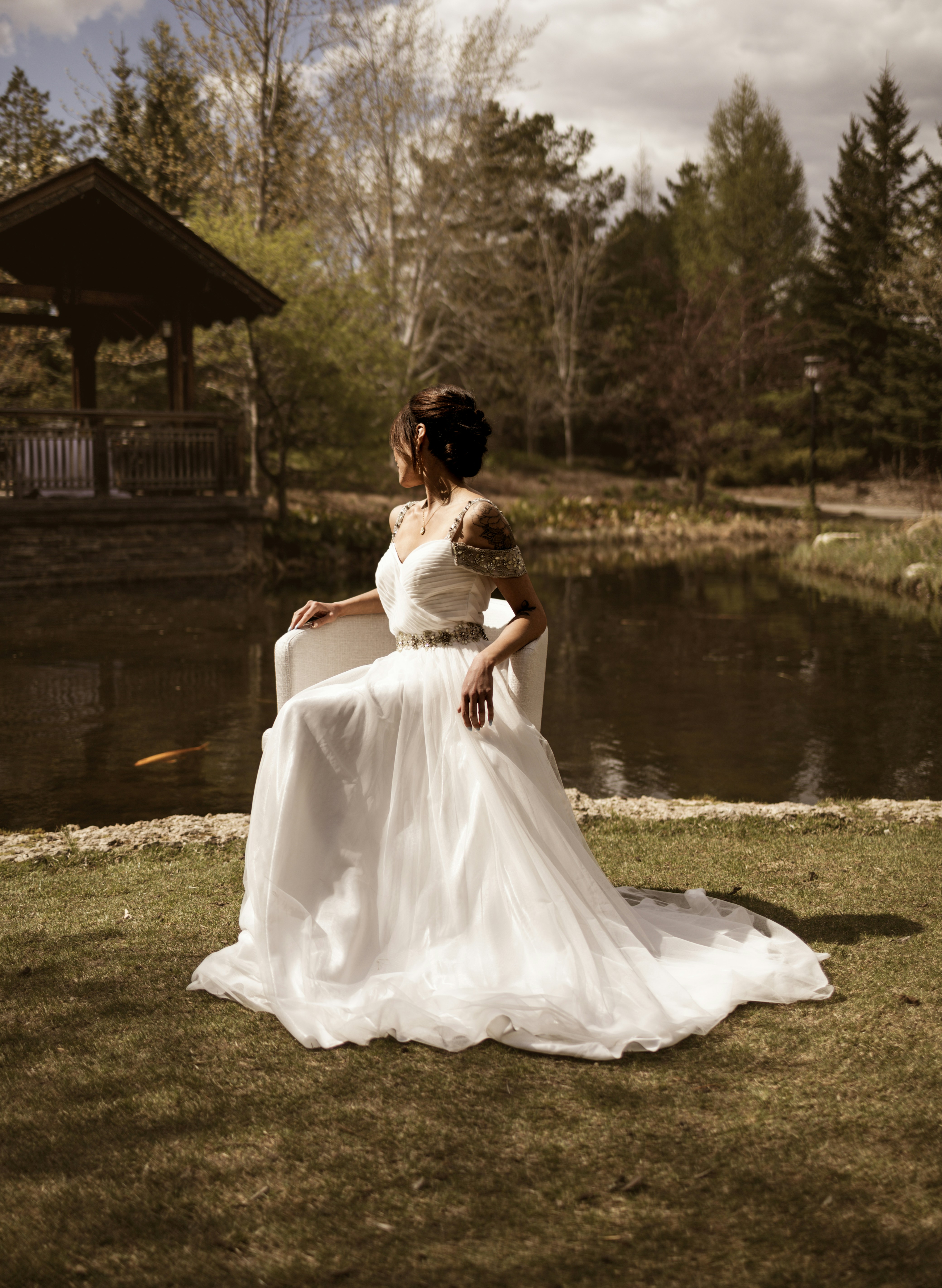 Bride in white dress sitting by pond