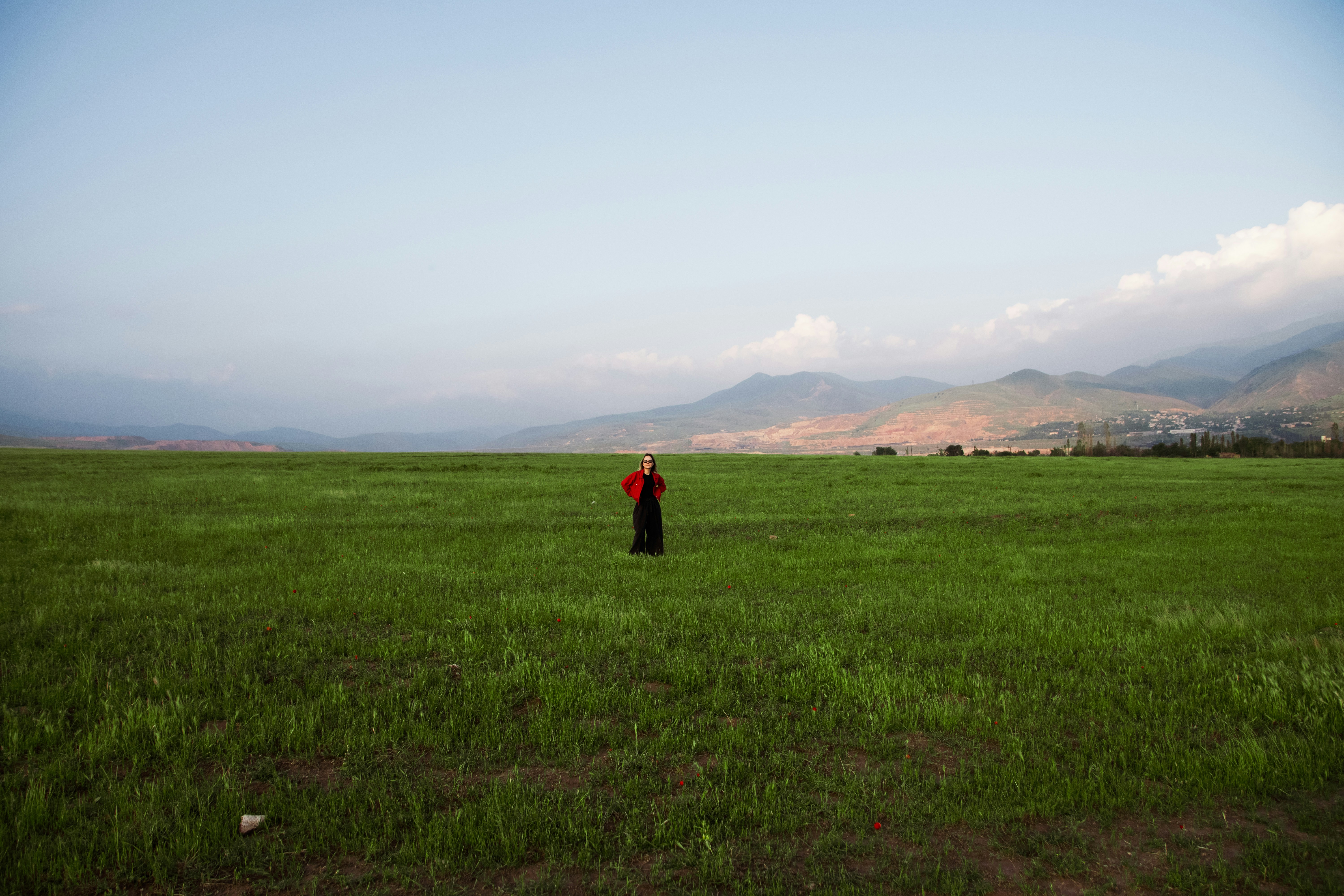 Red-vested Figure in Expansive Field Under Quiet Mountains