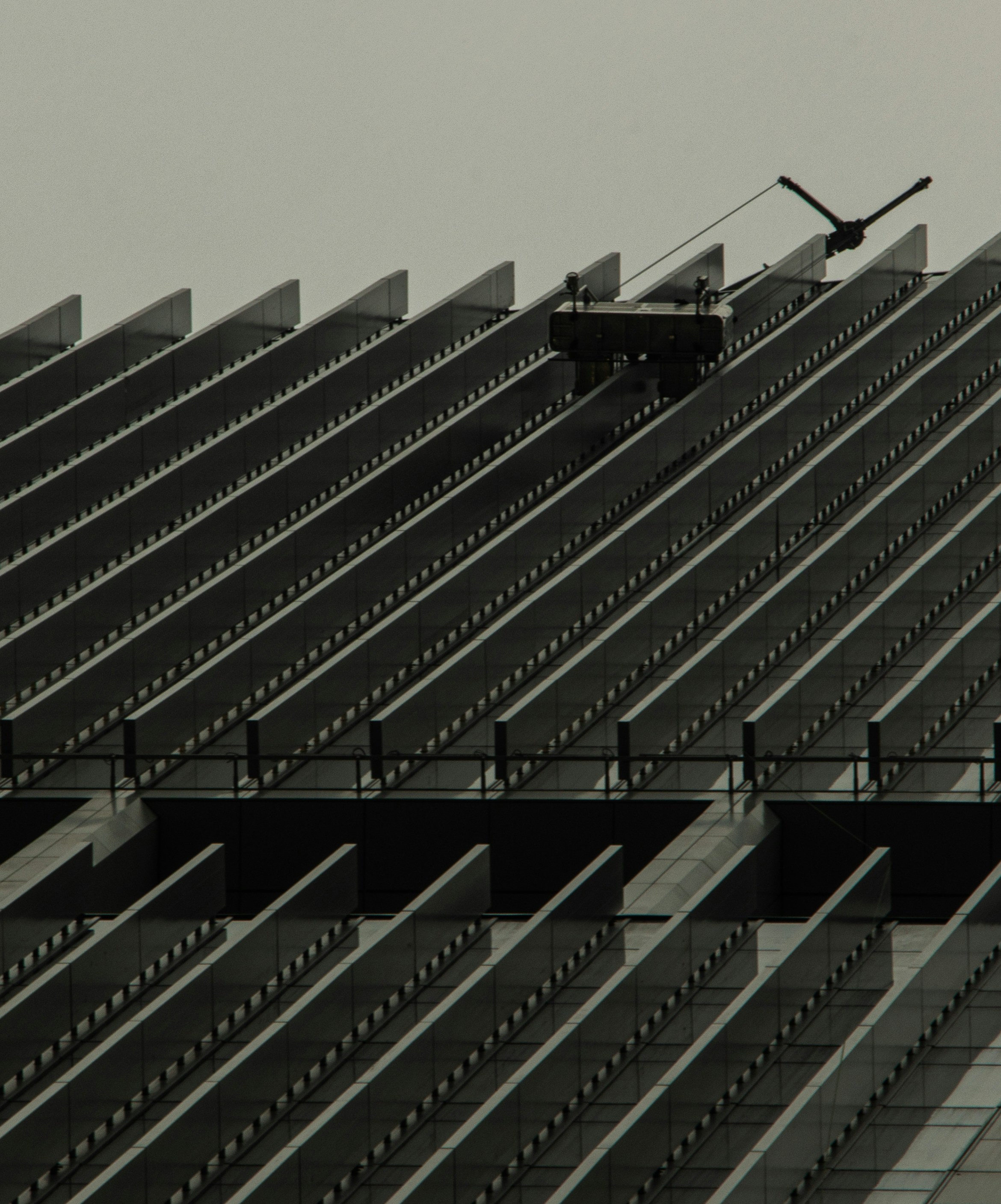 Crane silhouette atop a geometric, diagonal-slat roof structure with repeating horizontal lines. A minimal, architectural detail highlighting industrial texture and precision.