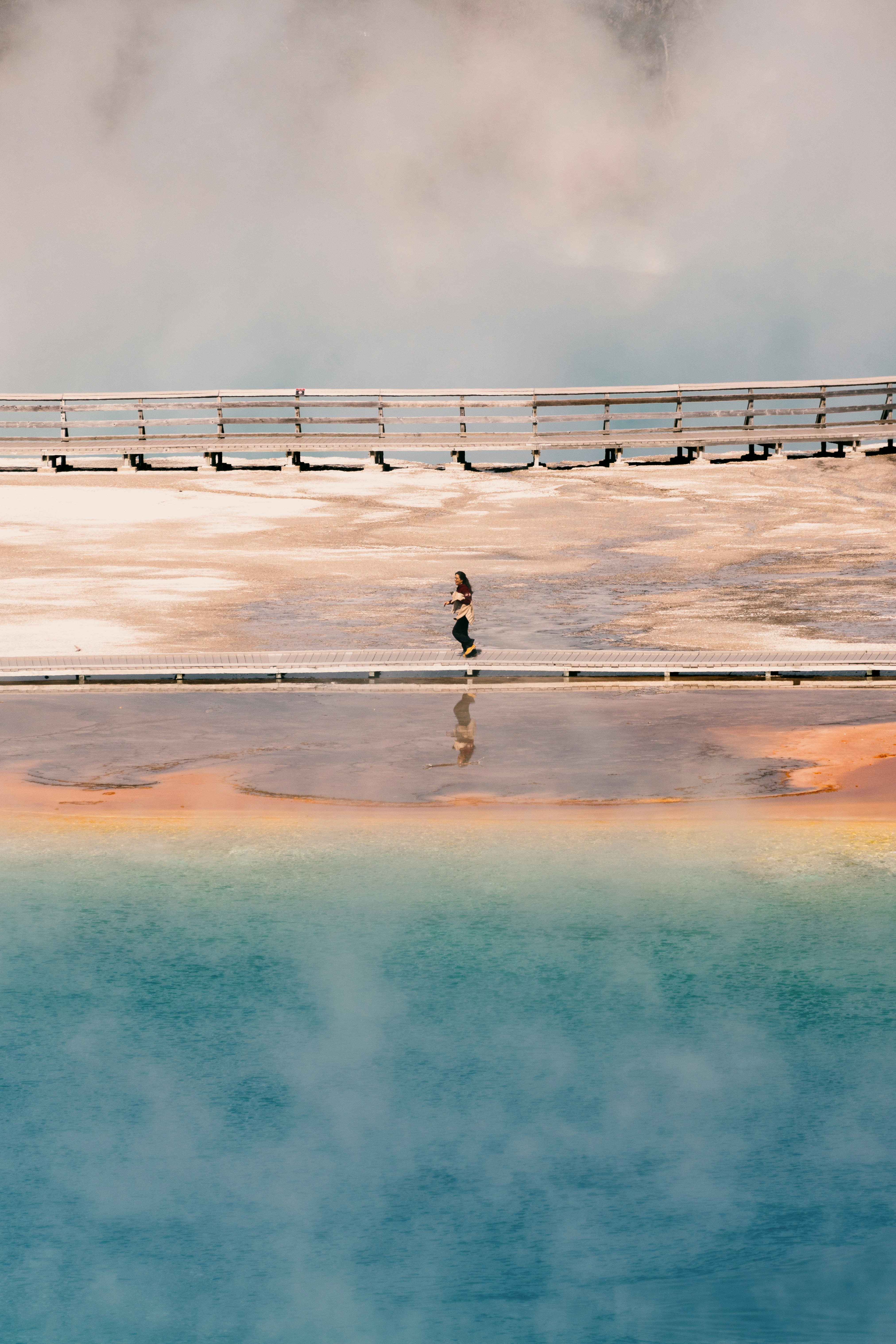 Single Walker on a Steam-tinged Boardwalk Over a Mineral Pool