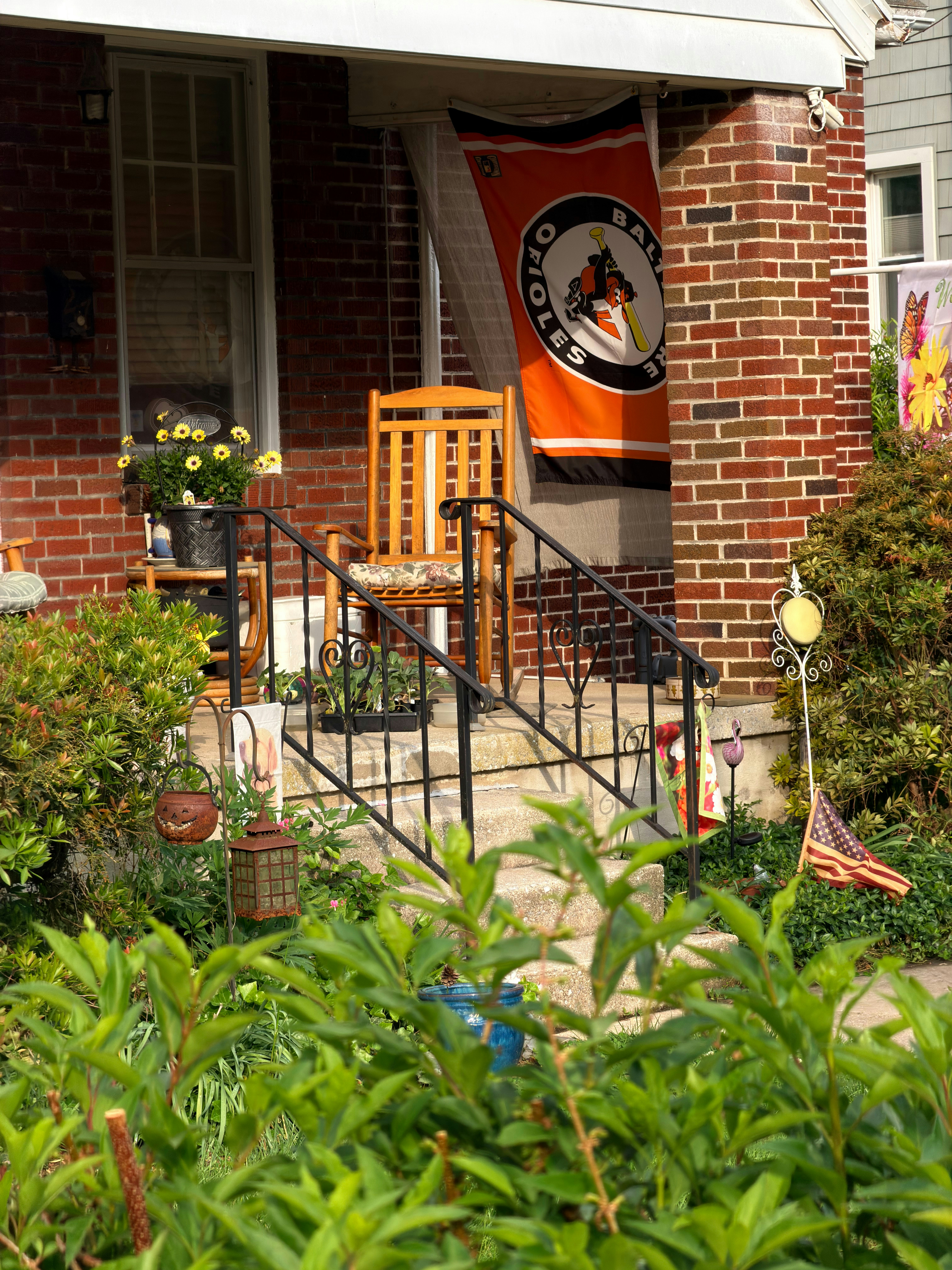 Front porch decorated with a rocking chair, plants, and flag.