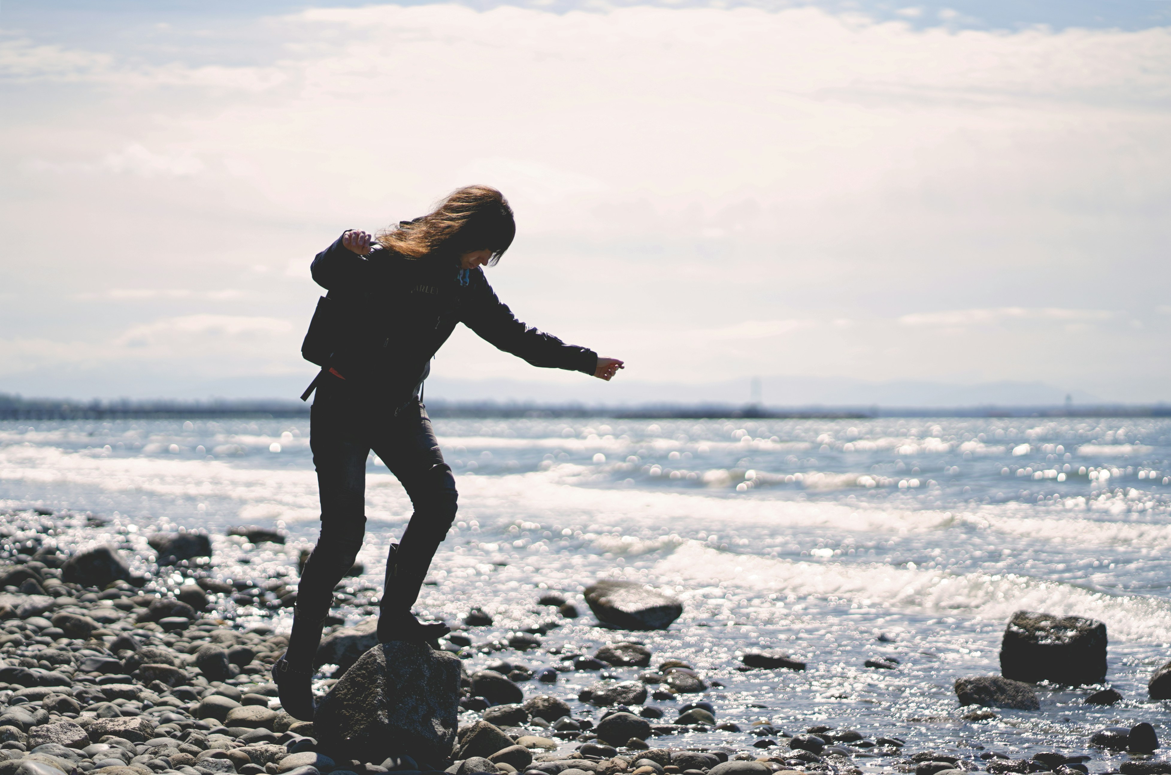 Balancer on the Shore: A lone figure test-steps the pebbled surf