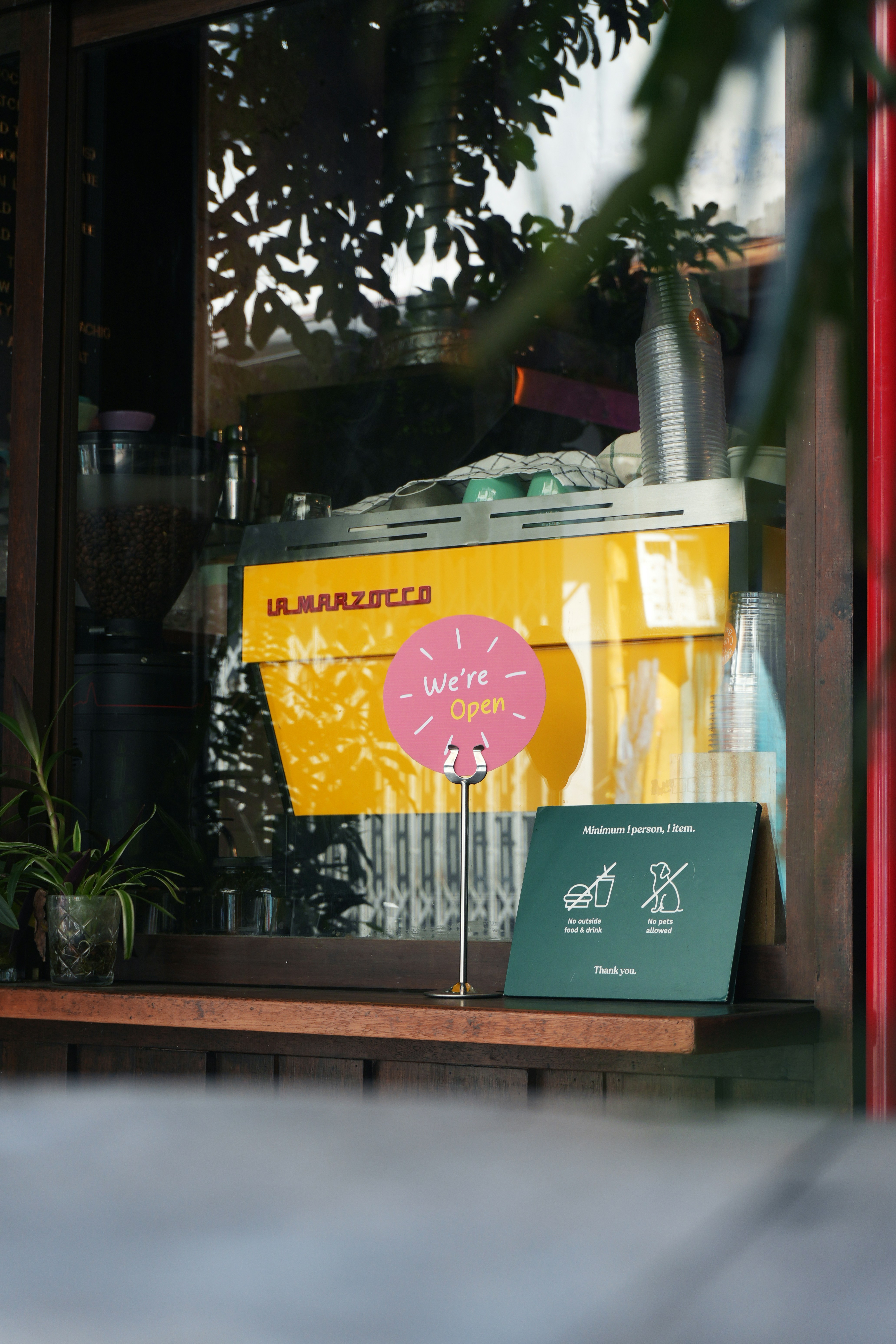 Bright pink sign in a cafe window signaling 'We're Open' among yellow vending/counter equipment