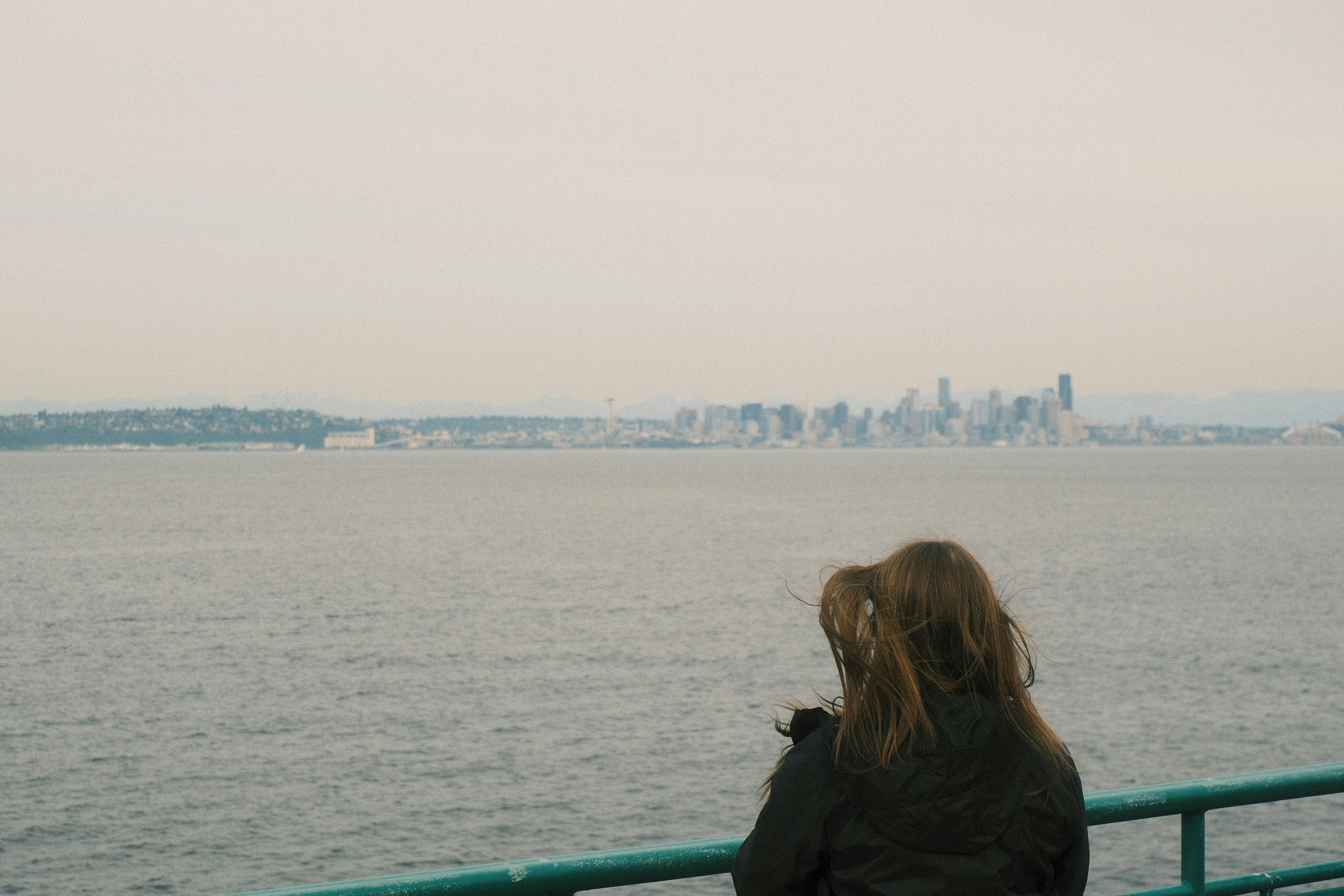 Woman on a ferry looking at a distant city skyline.