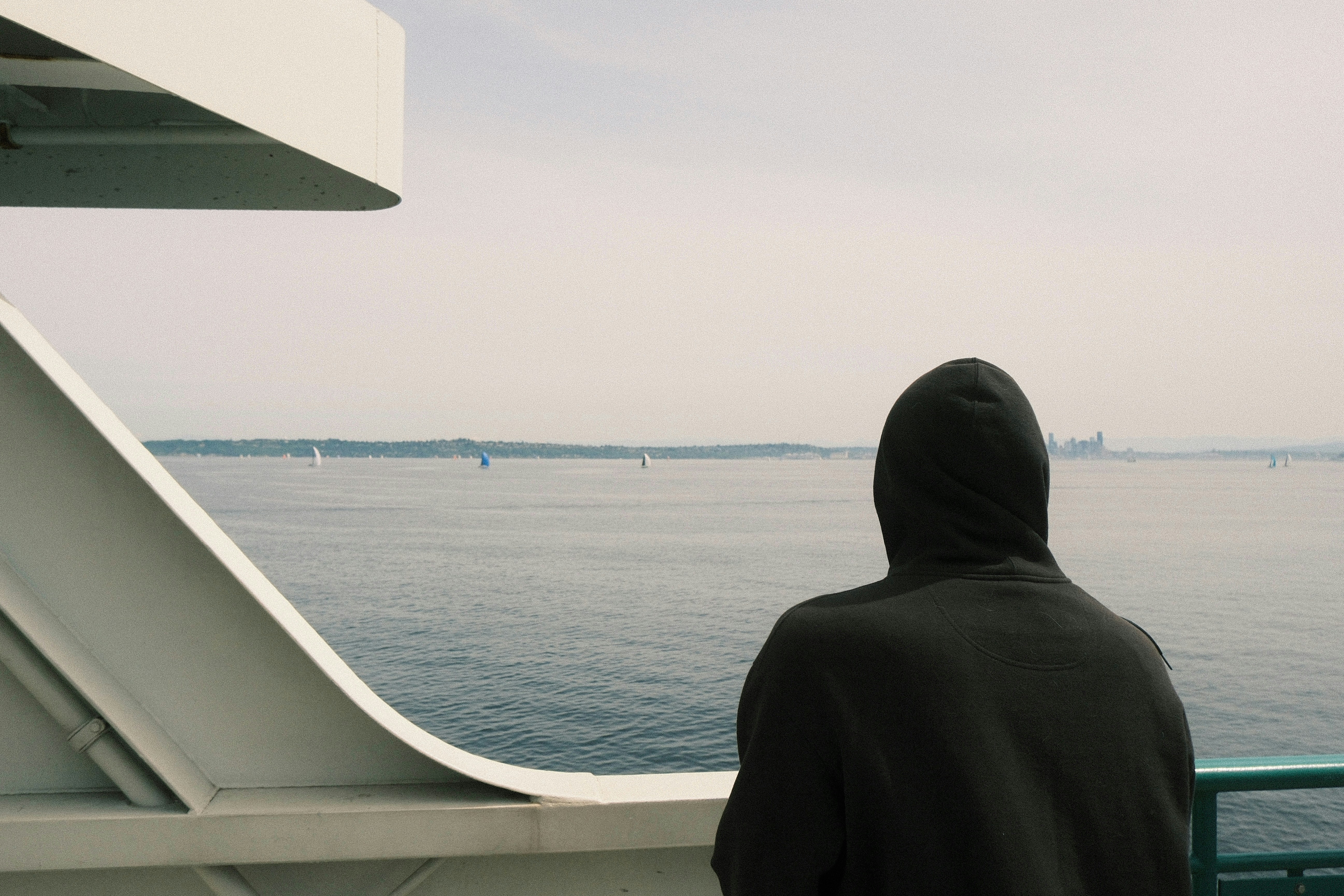Hooded figure at the railing watching a distant harbor