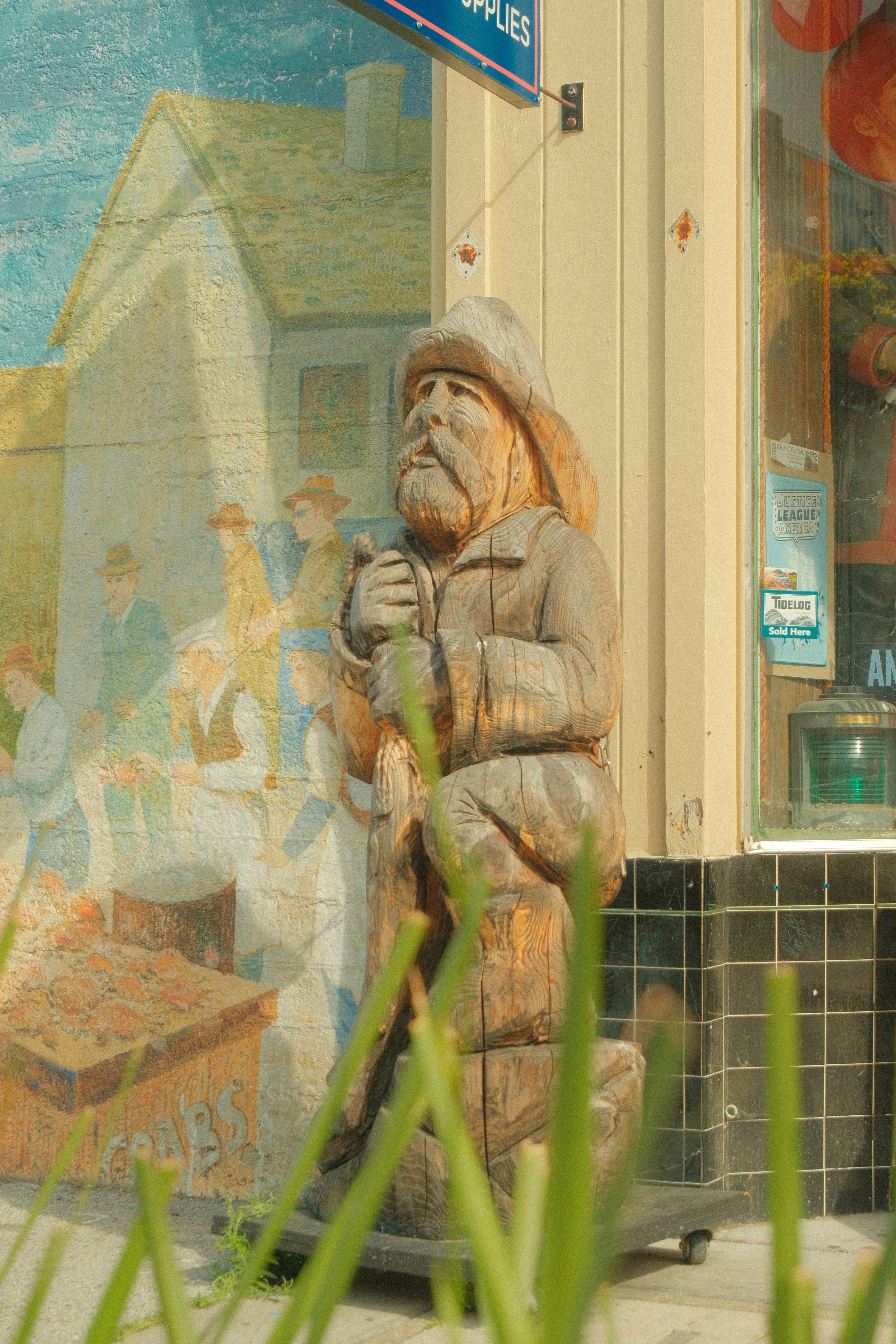 Weathered Wooden Statue Guards a Shop Window Like a Quiet Sentinel