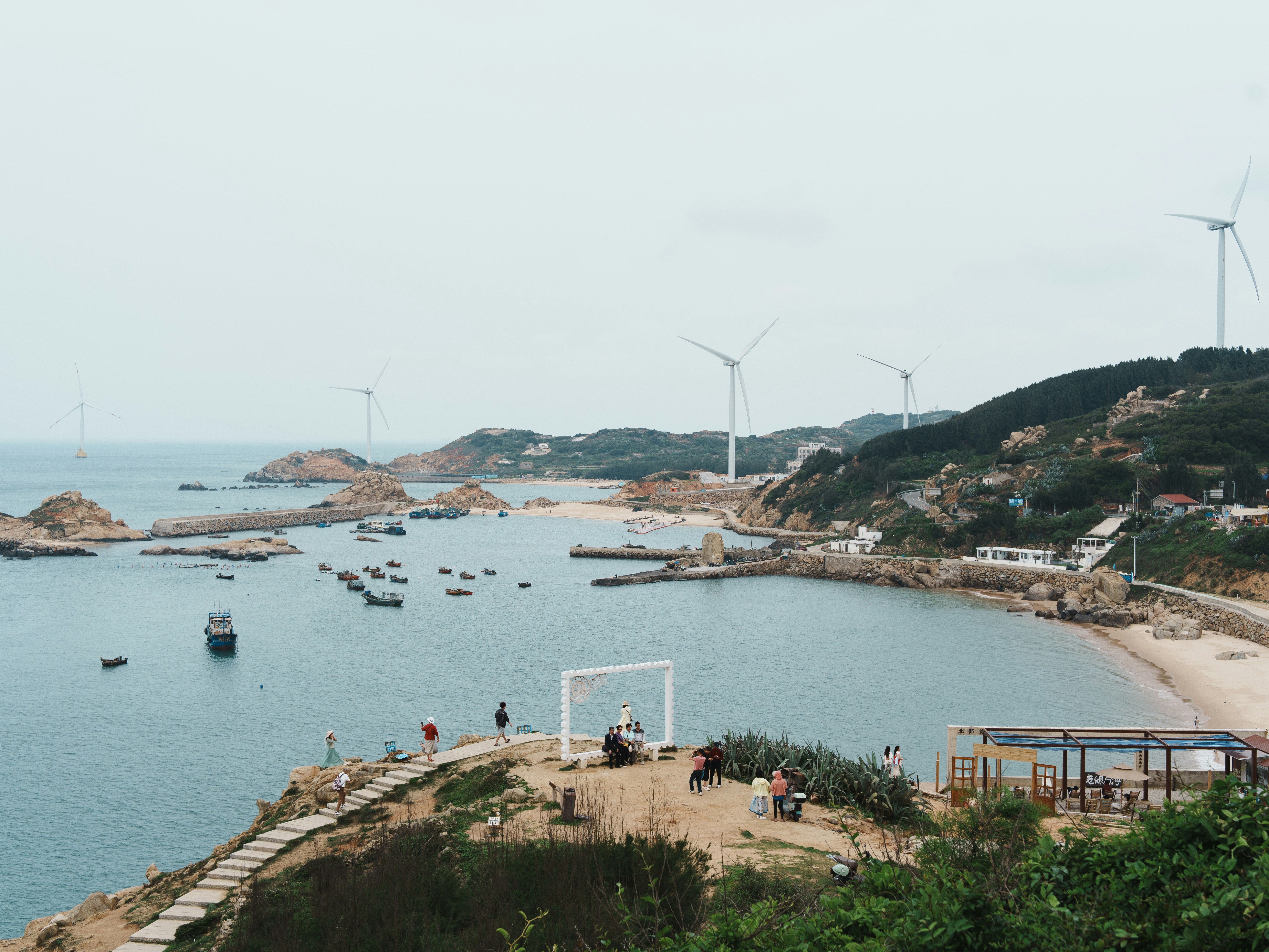 Wind-Swept Cove: Boats, Breakwater, and Turbine Silhouettes