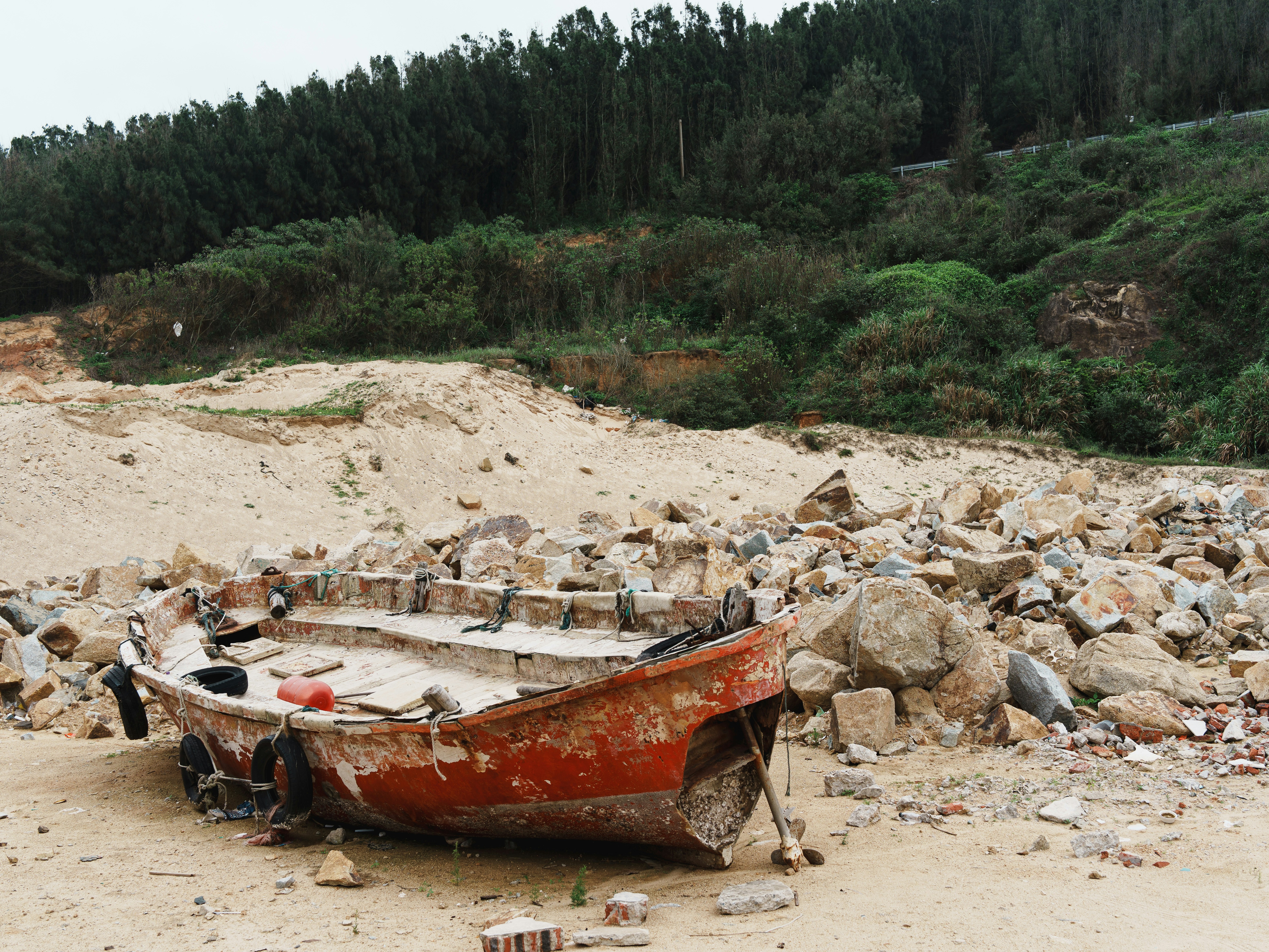 Weathered Red Boat on a Rocky Shore under Distant Trees