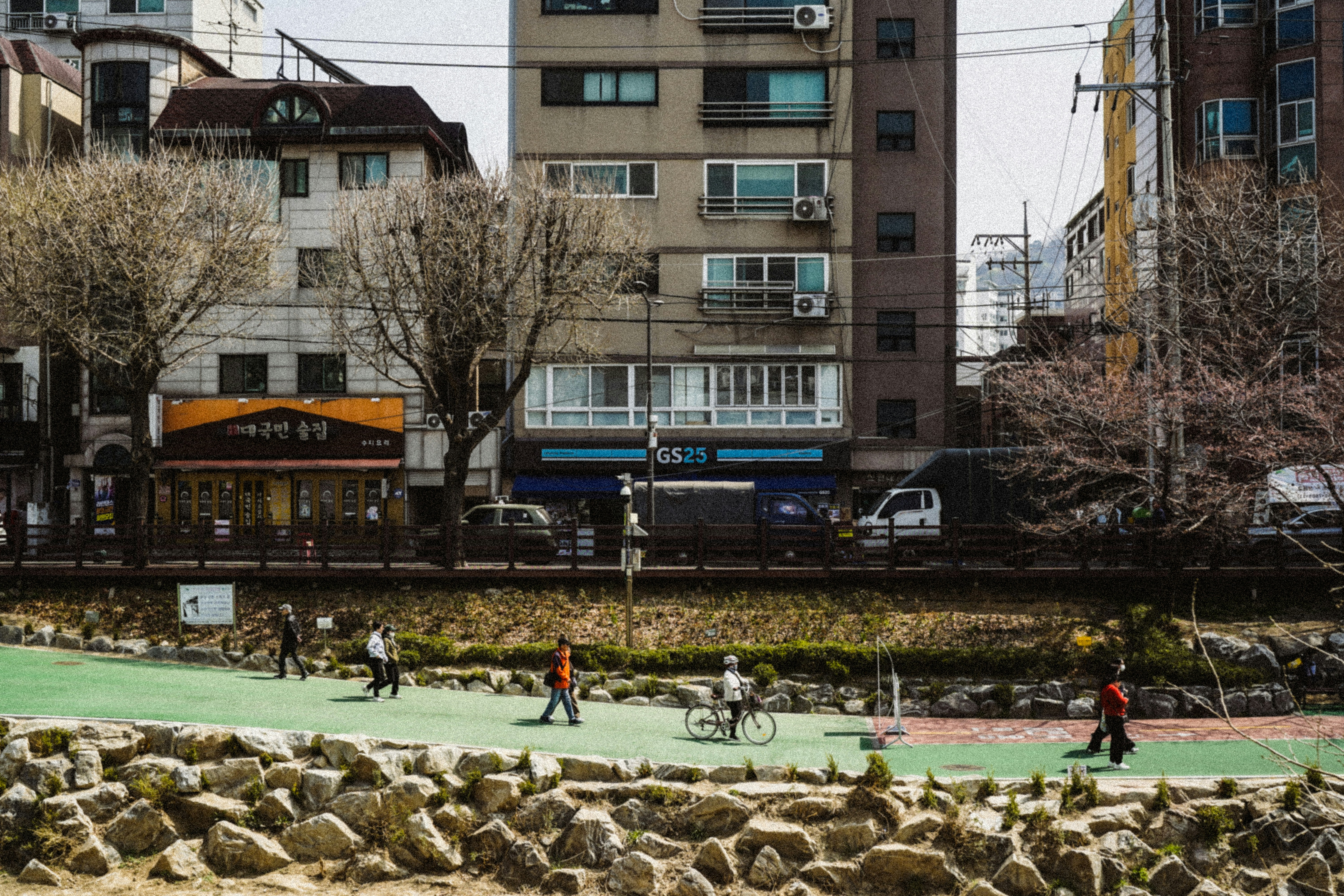 Urban Riverbank in Motion: A City Scene Framed by Aged Facades and Busy Path