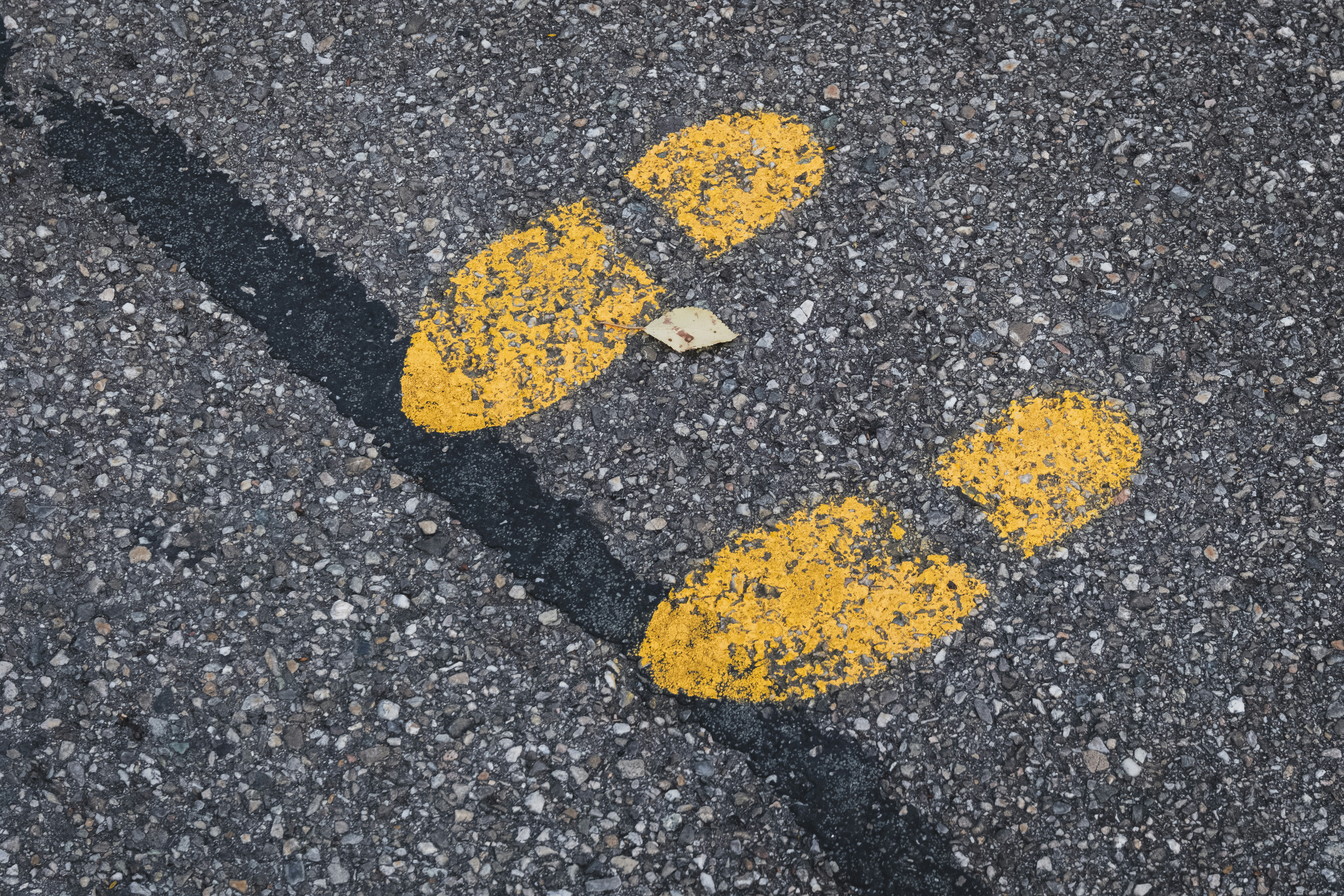 Yellow footprint markings on rough asphalt with a single leaf resting between the prints.