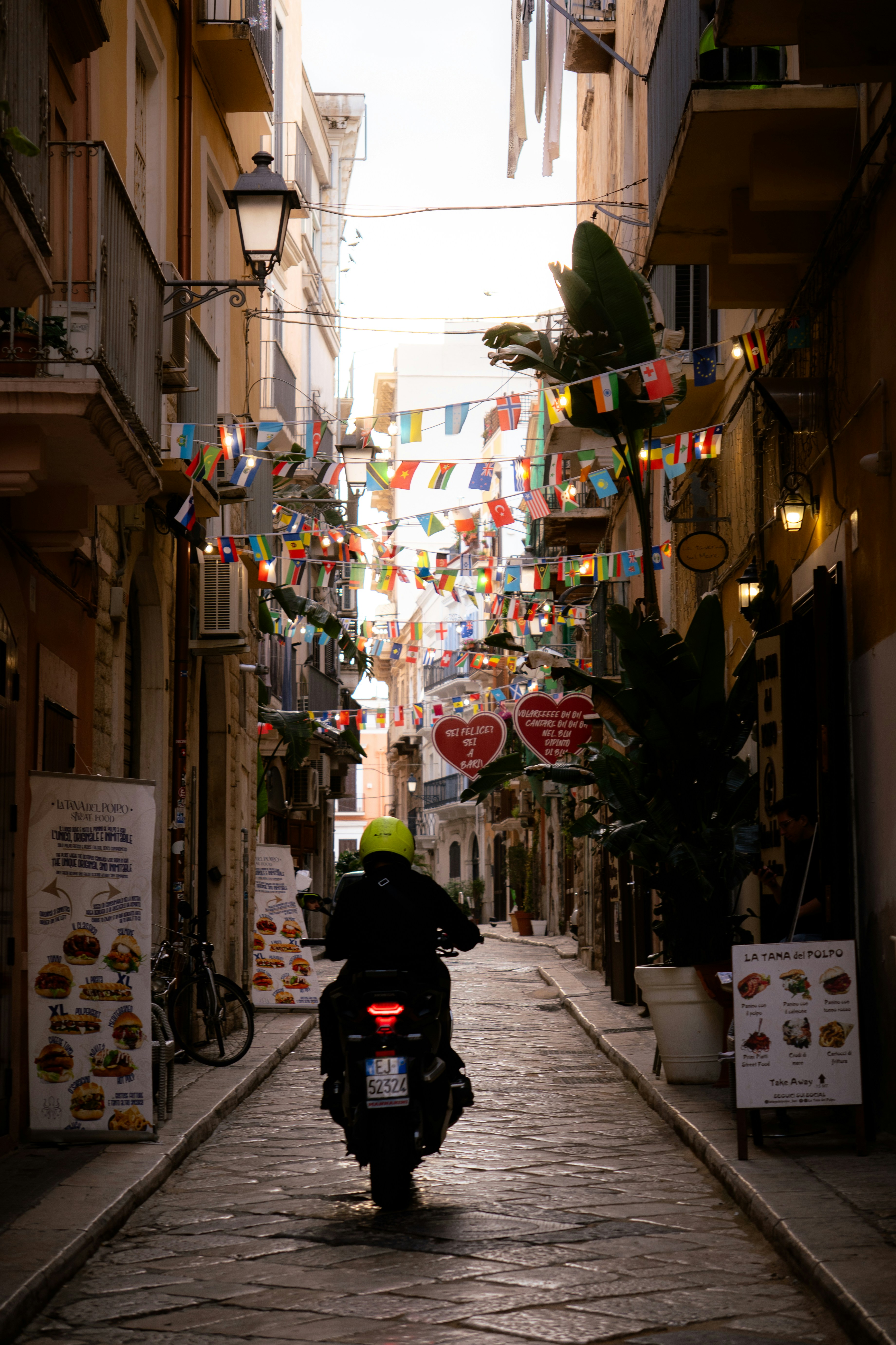 Rush Hour in a Woven Street: A Motorcycle Streak Beneath Colorful Flags