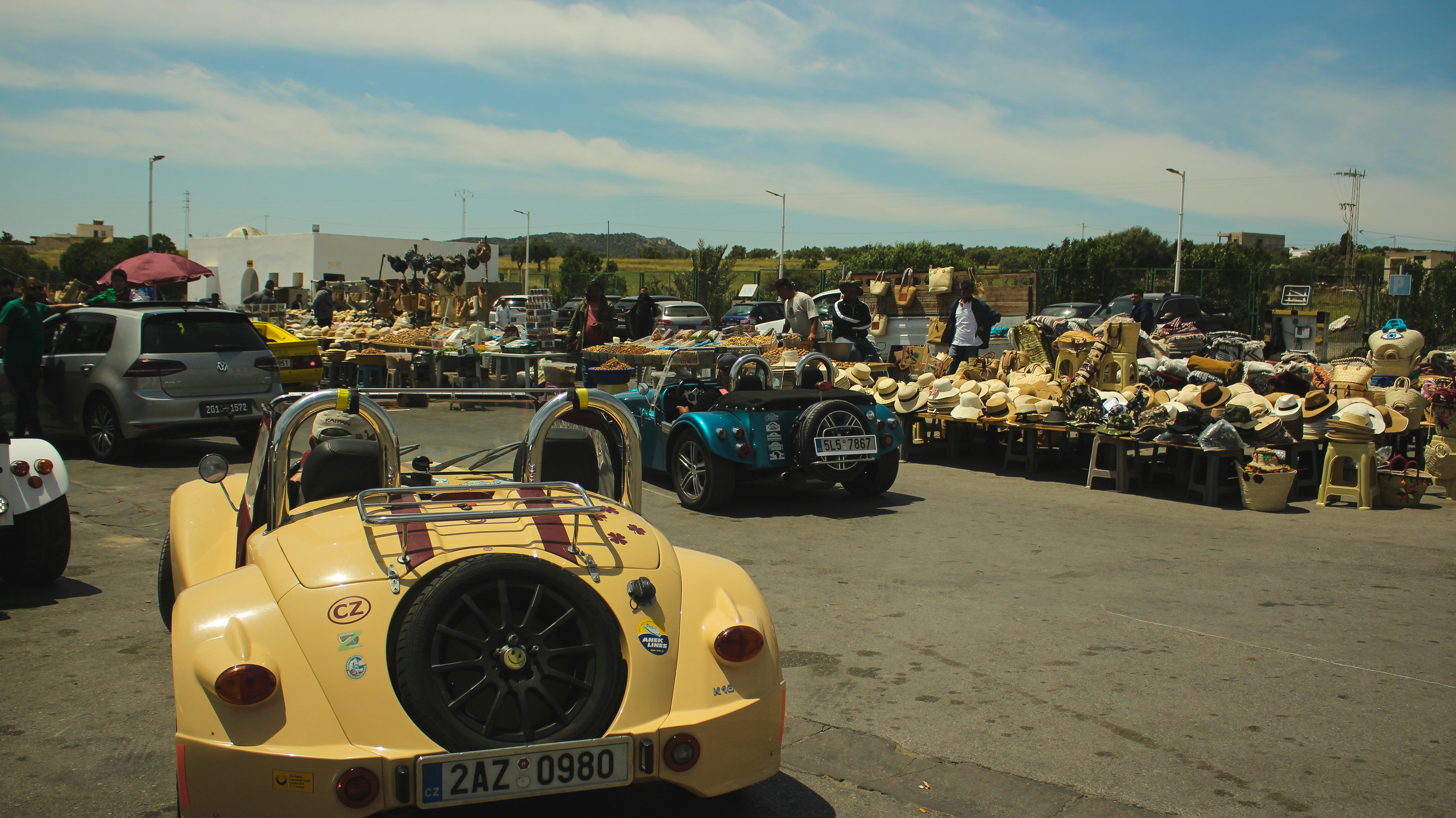 Yellow vintage sports car at a sunlit outdoor market