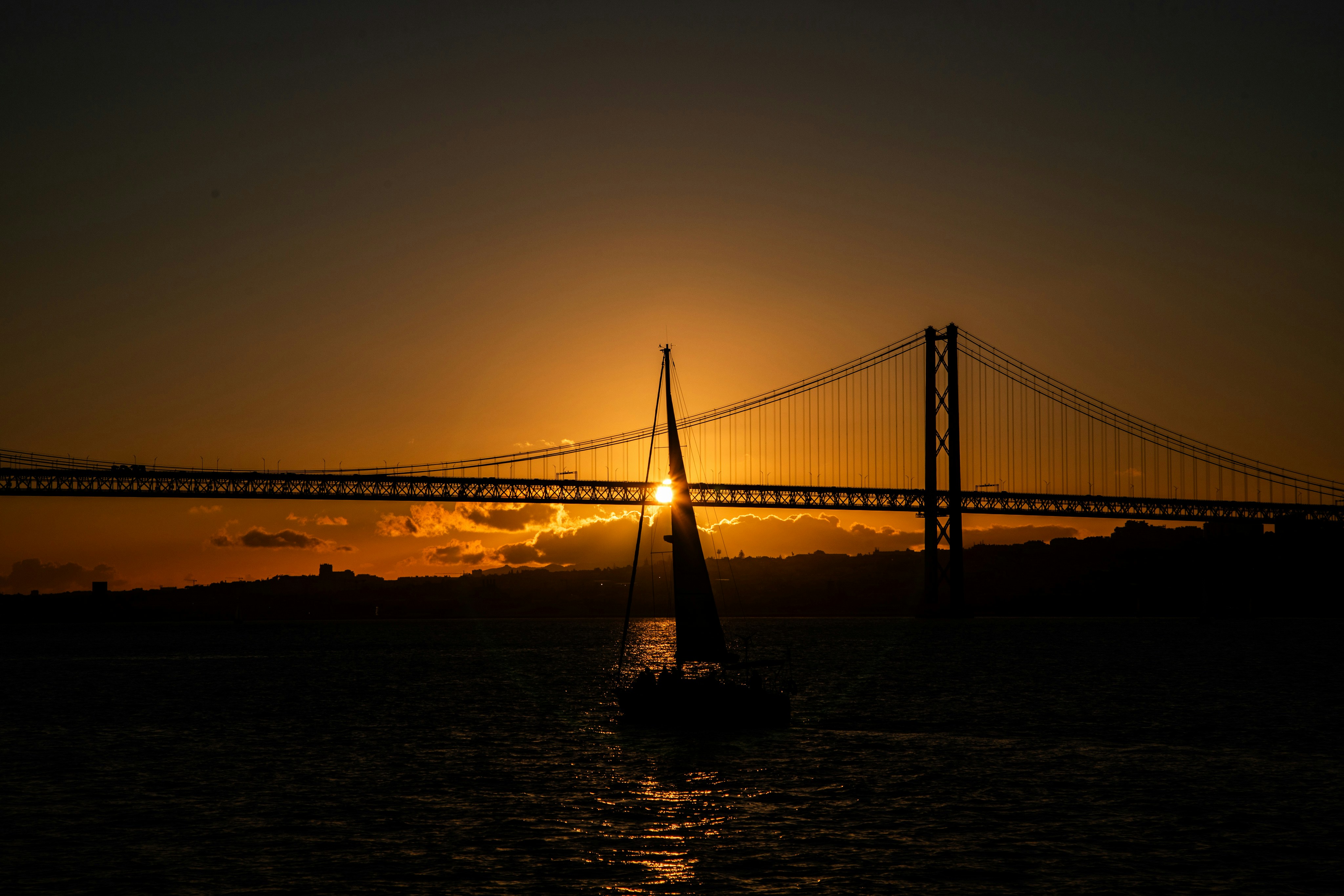 Sunlit Sail: silhouette of a boat under a suspended bridge at dusk