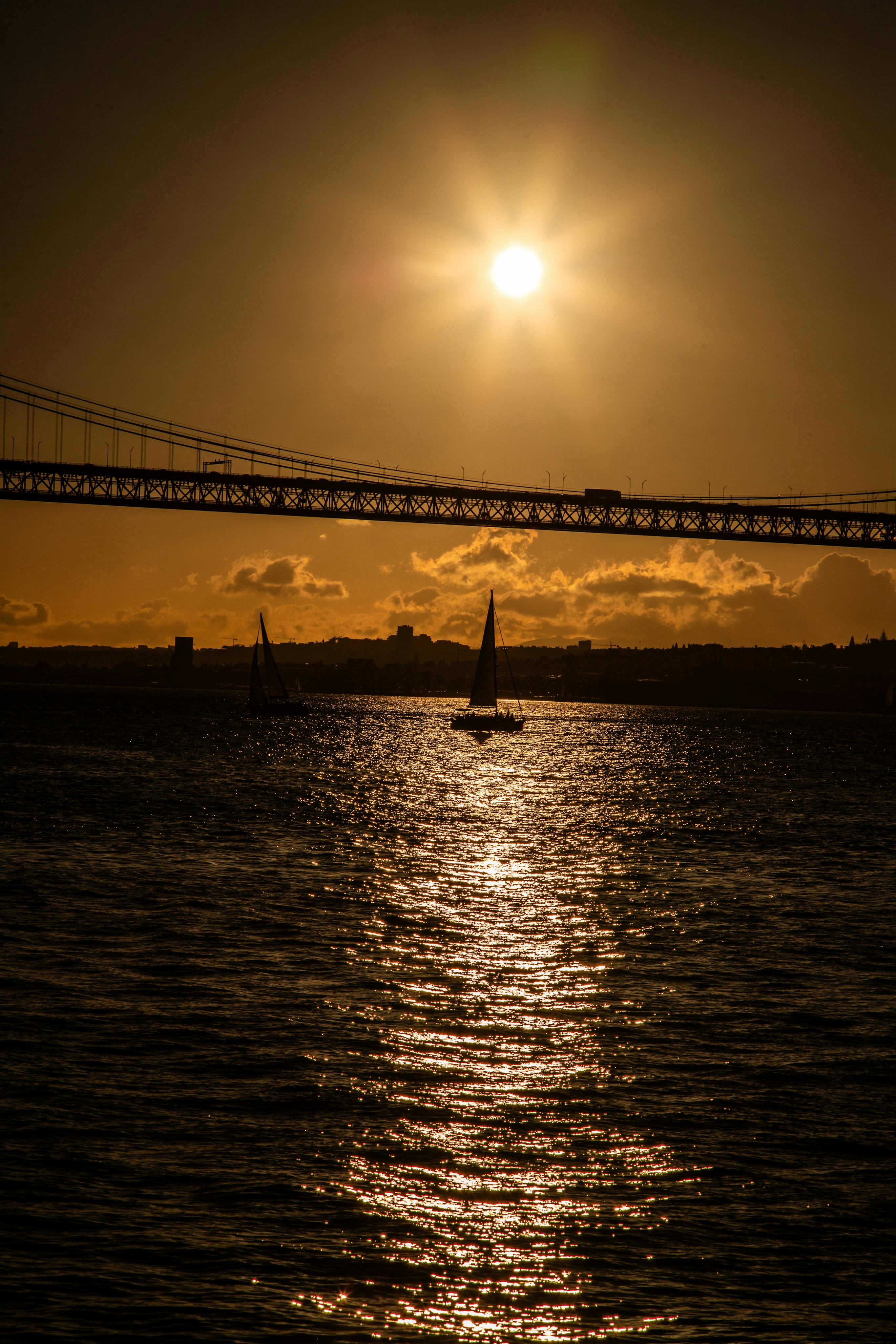 Golden Hour Over the River: Sailboats Beneath the Silhouette Bridge