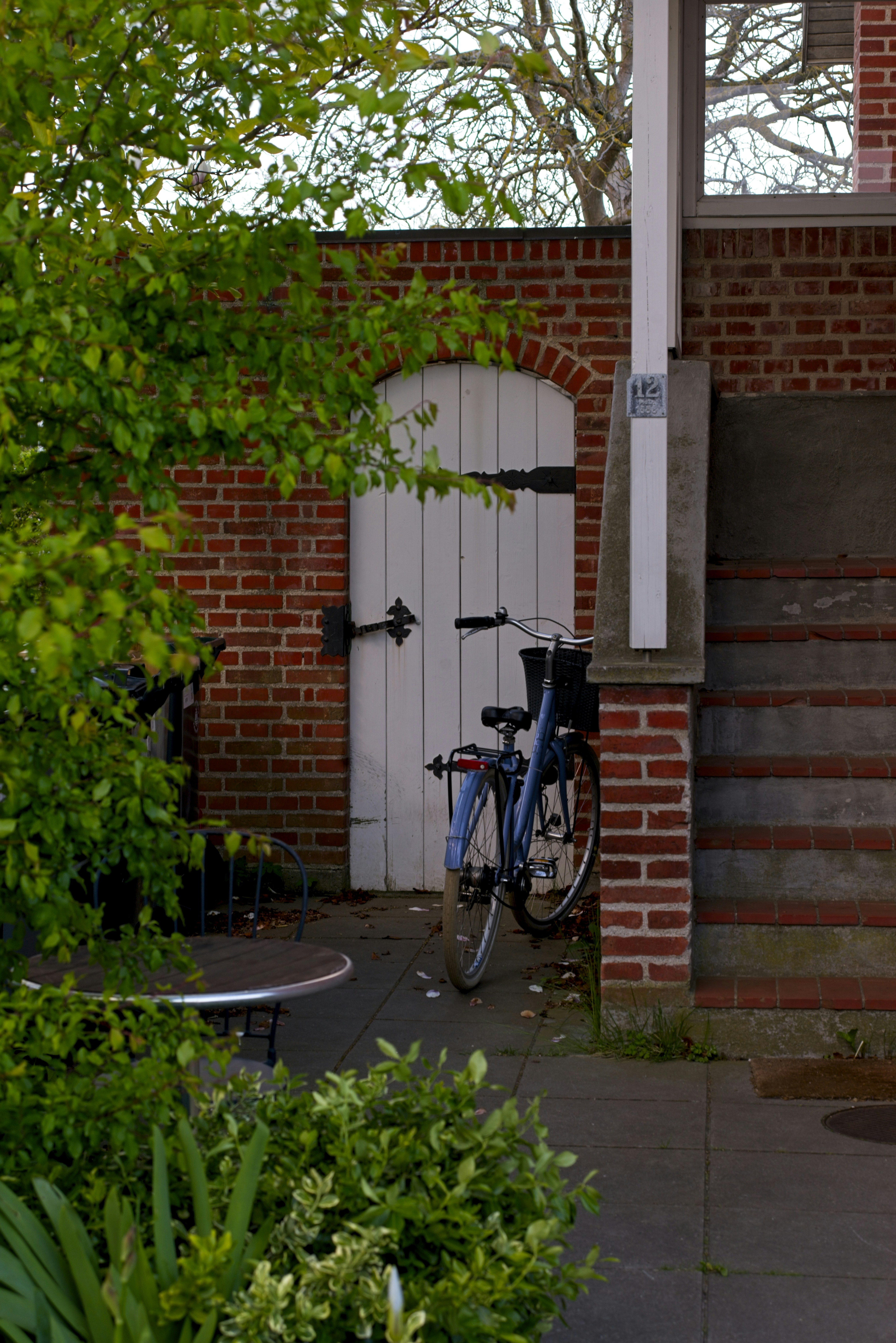 Bike Leaning Against a Brick Stairwell by a White Gate