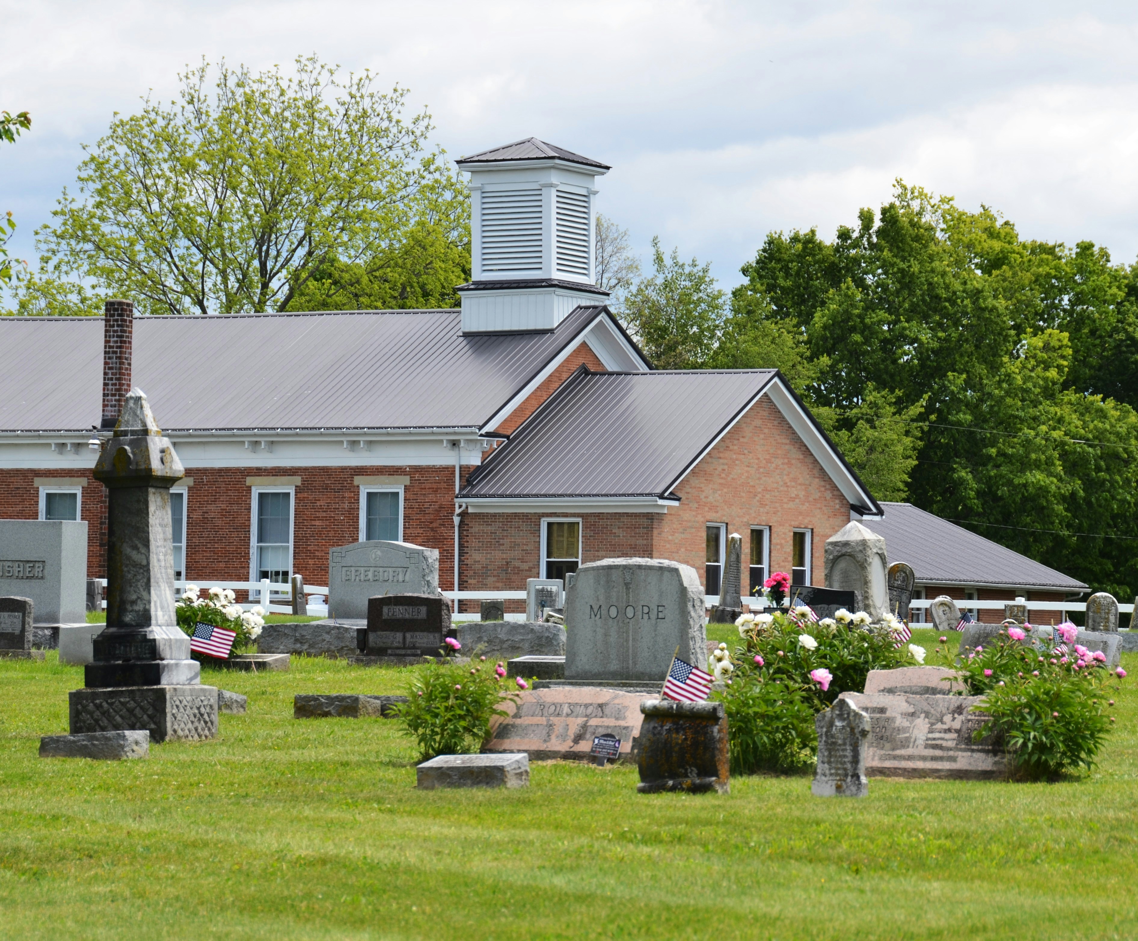 Cemetery Quiet at Dusk: A Brick Hall and Headstones Beyond the Lawn