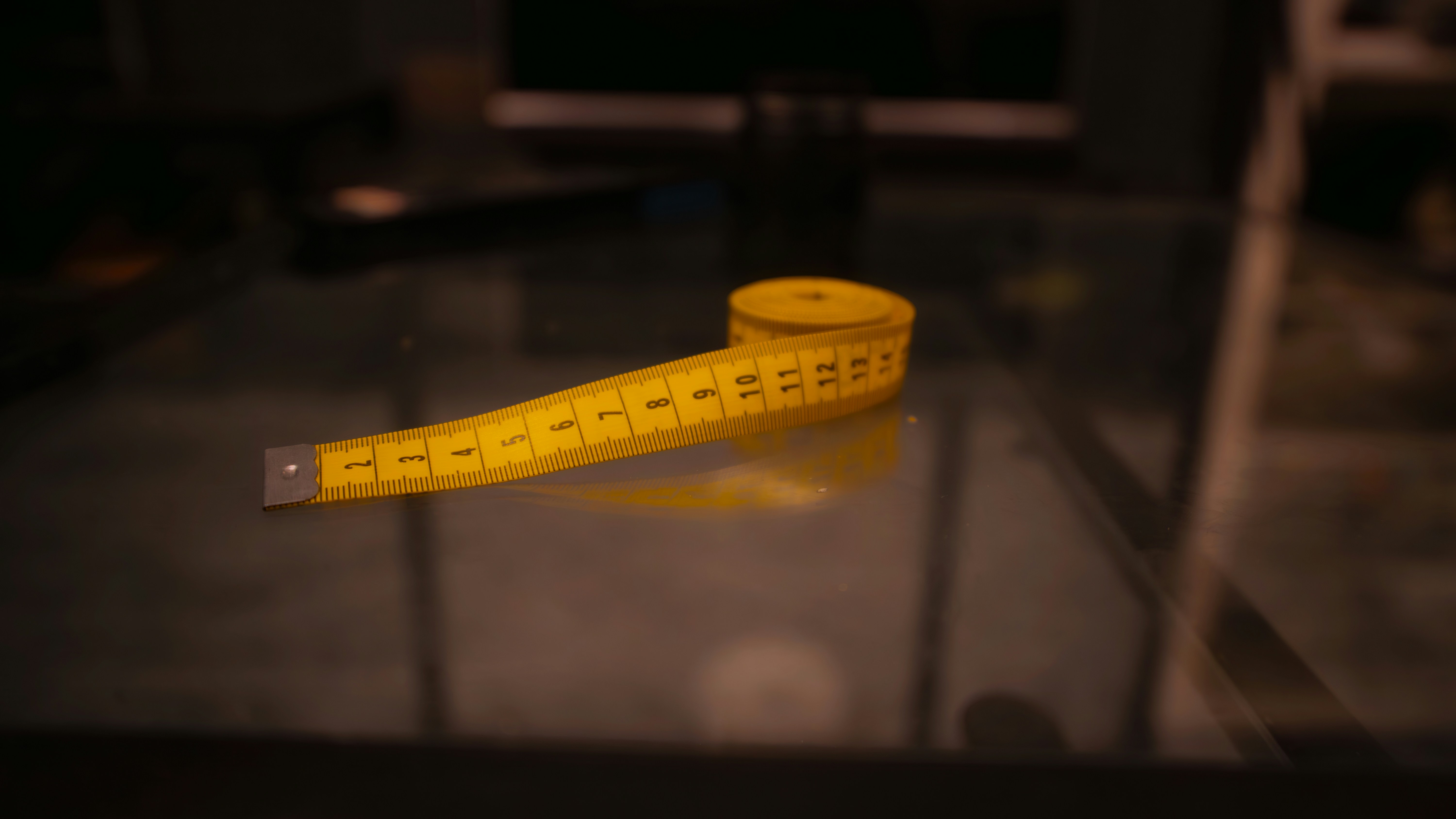 Unwinding Precision: A Yellow Measuring Tape on a Glass Table