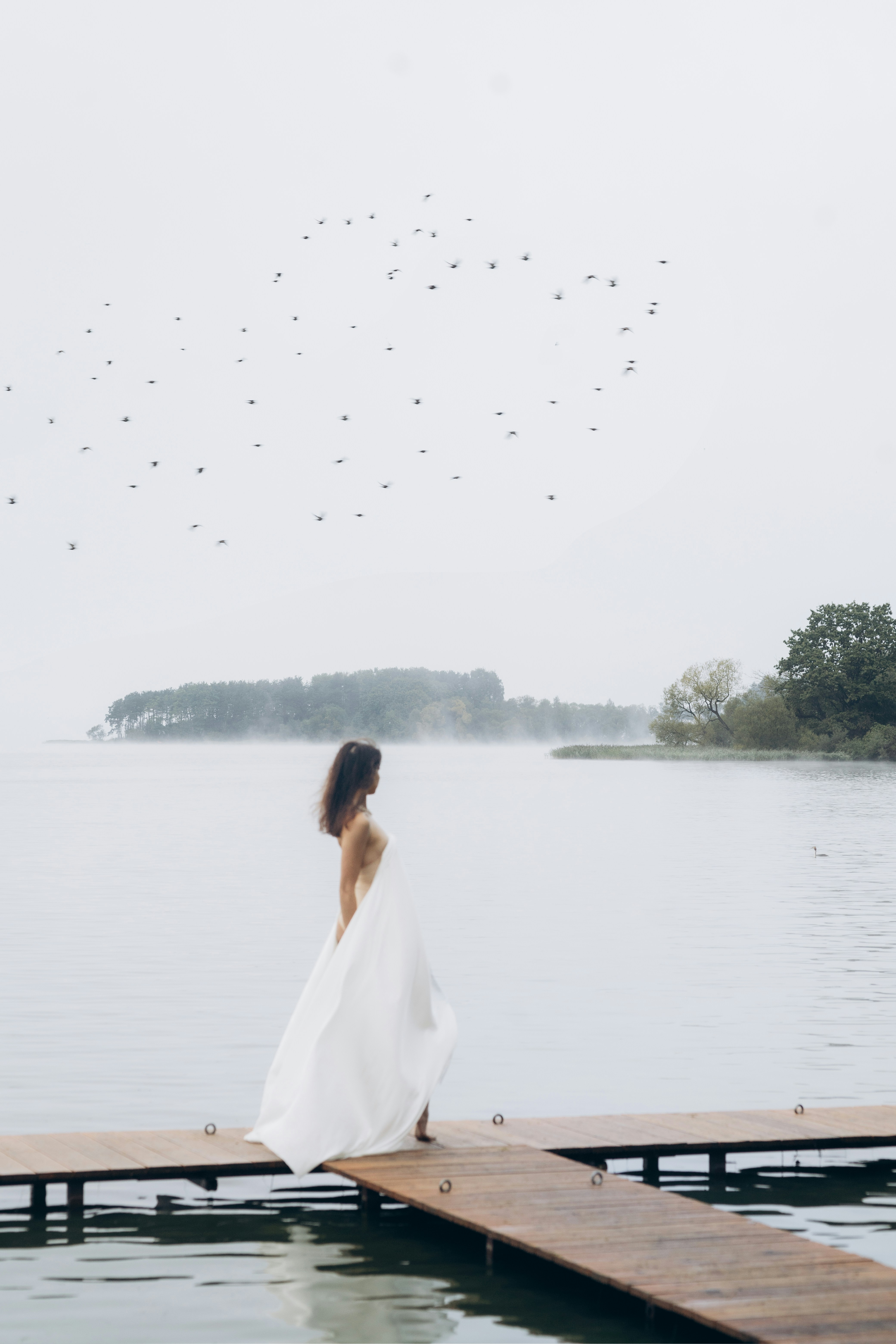 Quiet Bride on the Pier as Birds Scatter Over Misty Lake