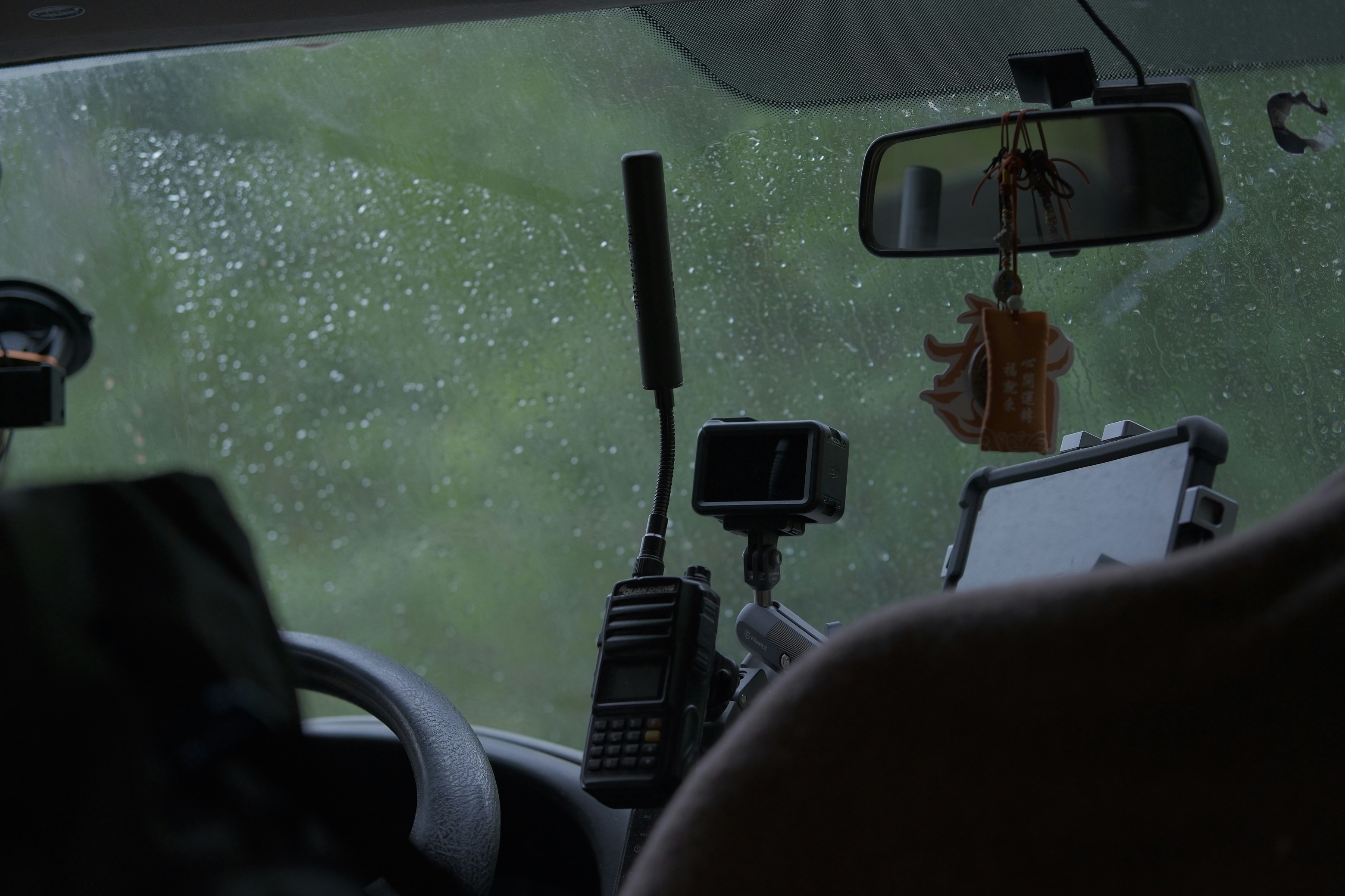 Vehicle cockpit at dusk: gear, screens, and rain-dotted windshield